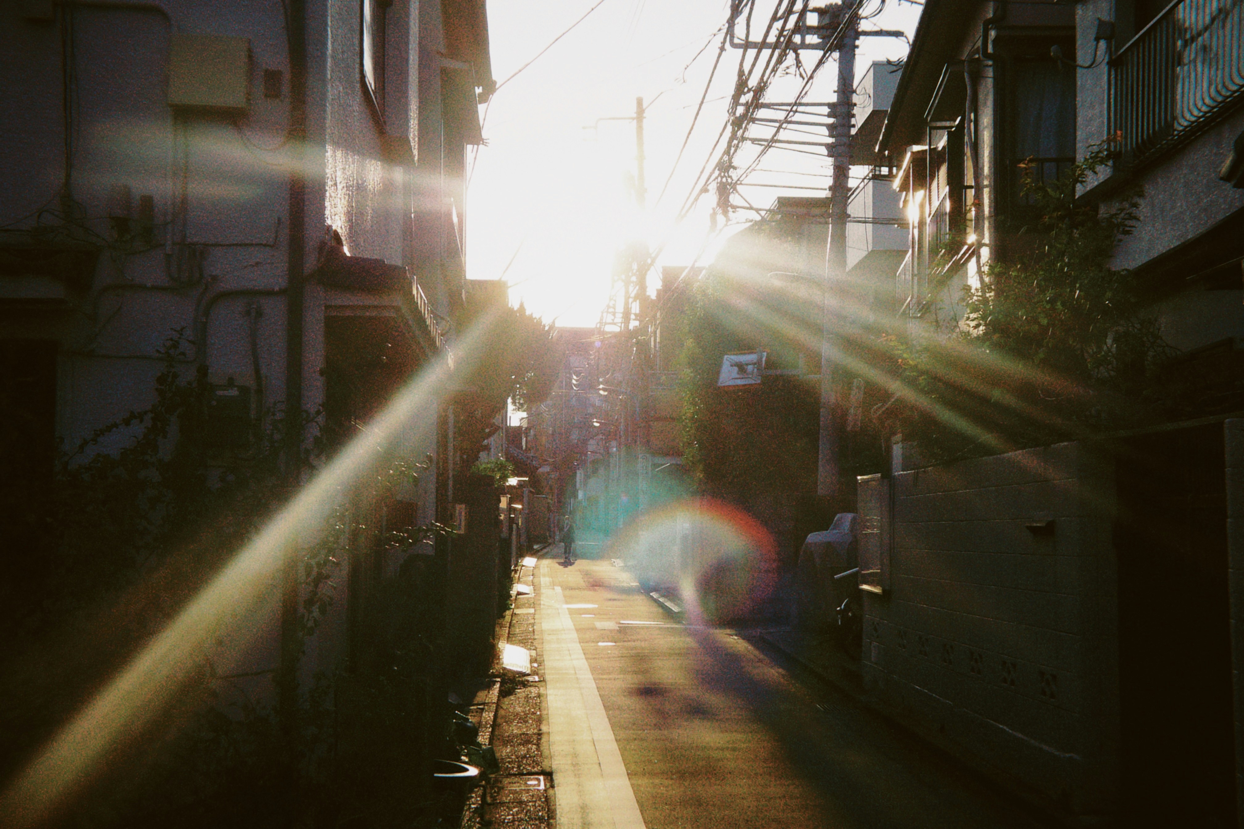 Sunlight streams down a narrow street between buildings.