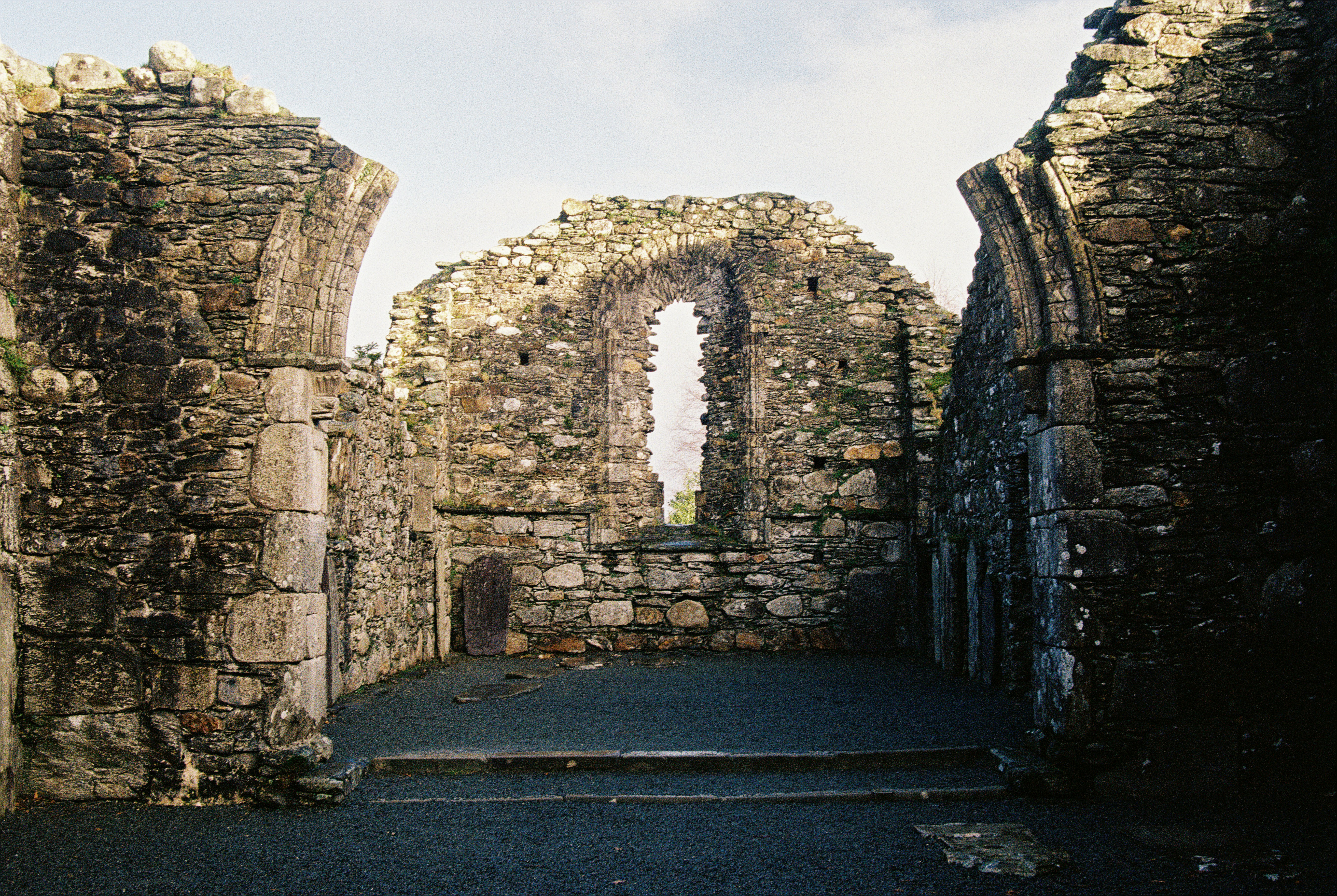 Historic stone ruins of an ancient church featuring weathered Gothic arch windows and crumbling medieval walls. The site reveals centuries of sacred architecture, with moss-covered stones and timeless craftsmanship. A captivating glimpse into history, spirituality, and heritage, perfect for travelers seeking cultural landmarks and atmospheric photography. | Ancient stone ruins with arched window against sky