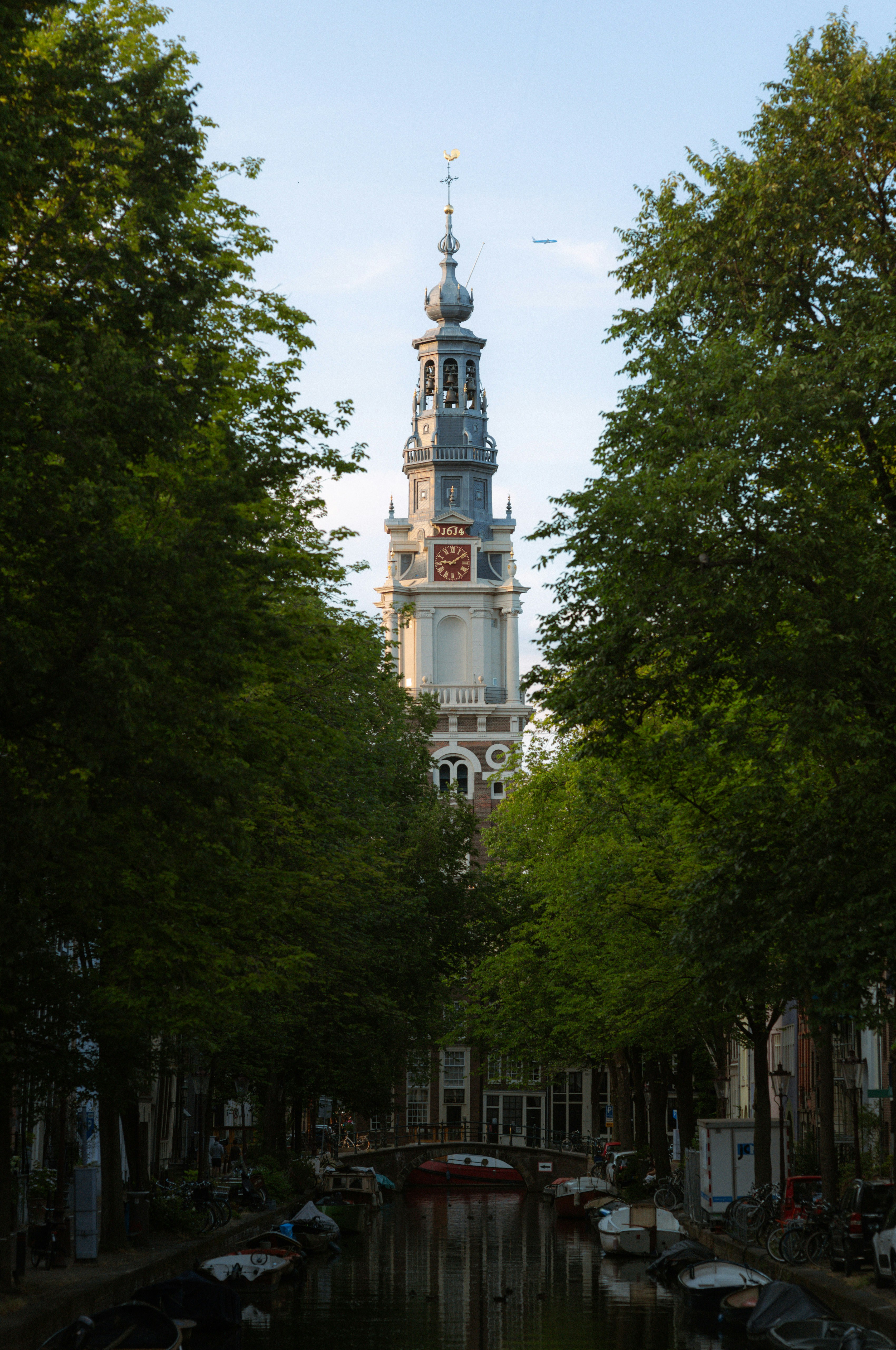 Tall church tower framed by green trees and canal.