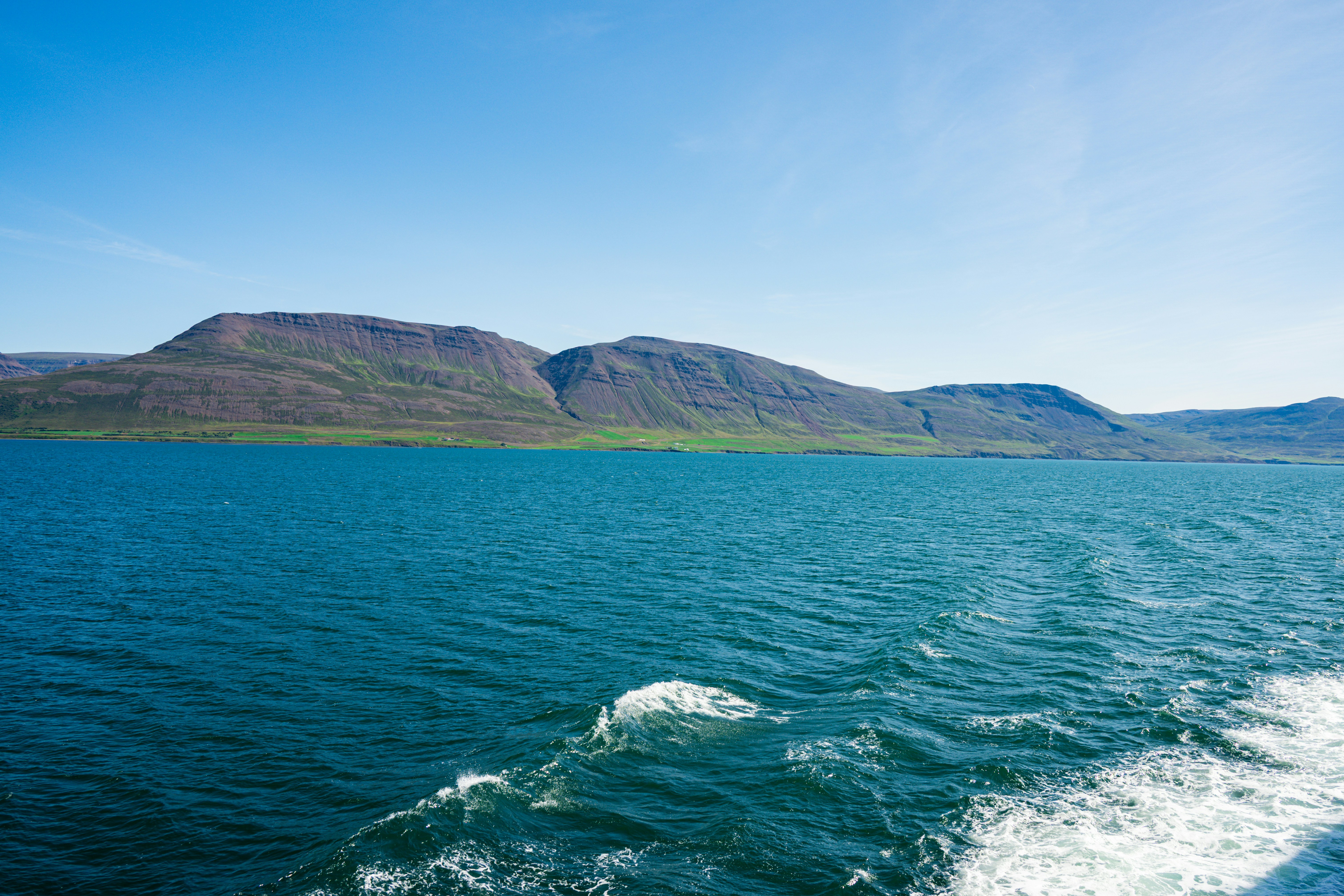 Blue ocean water with distant green mountains under a clear sky