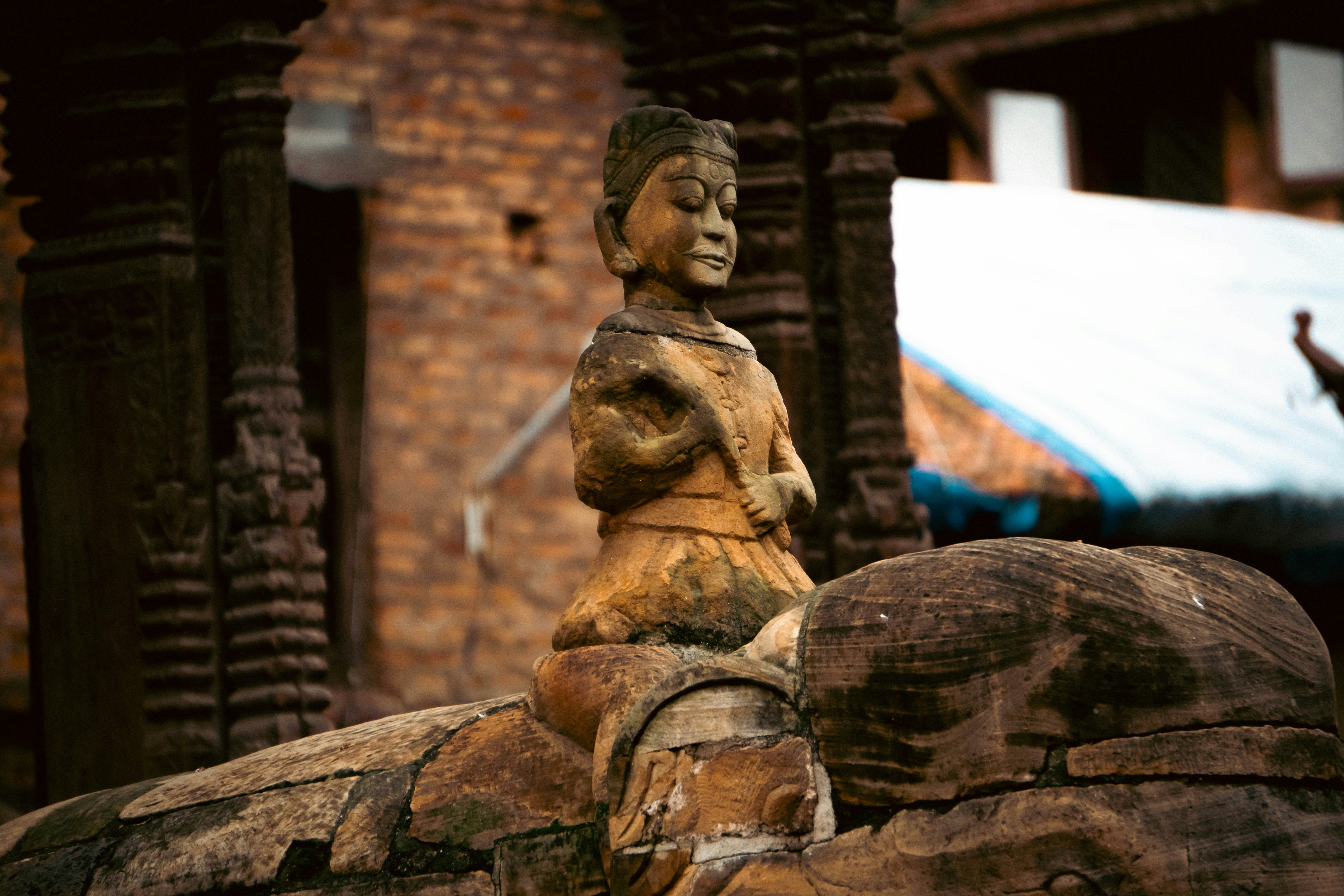 Ancient stone sculpture of a serene figure seated atop a weathered log, surrounded by historical architecture.