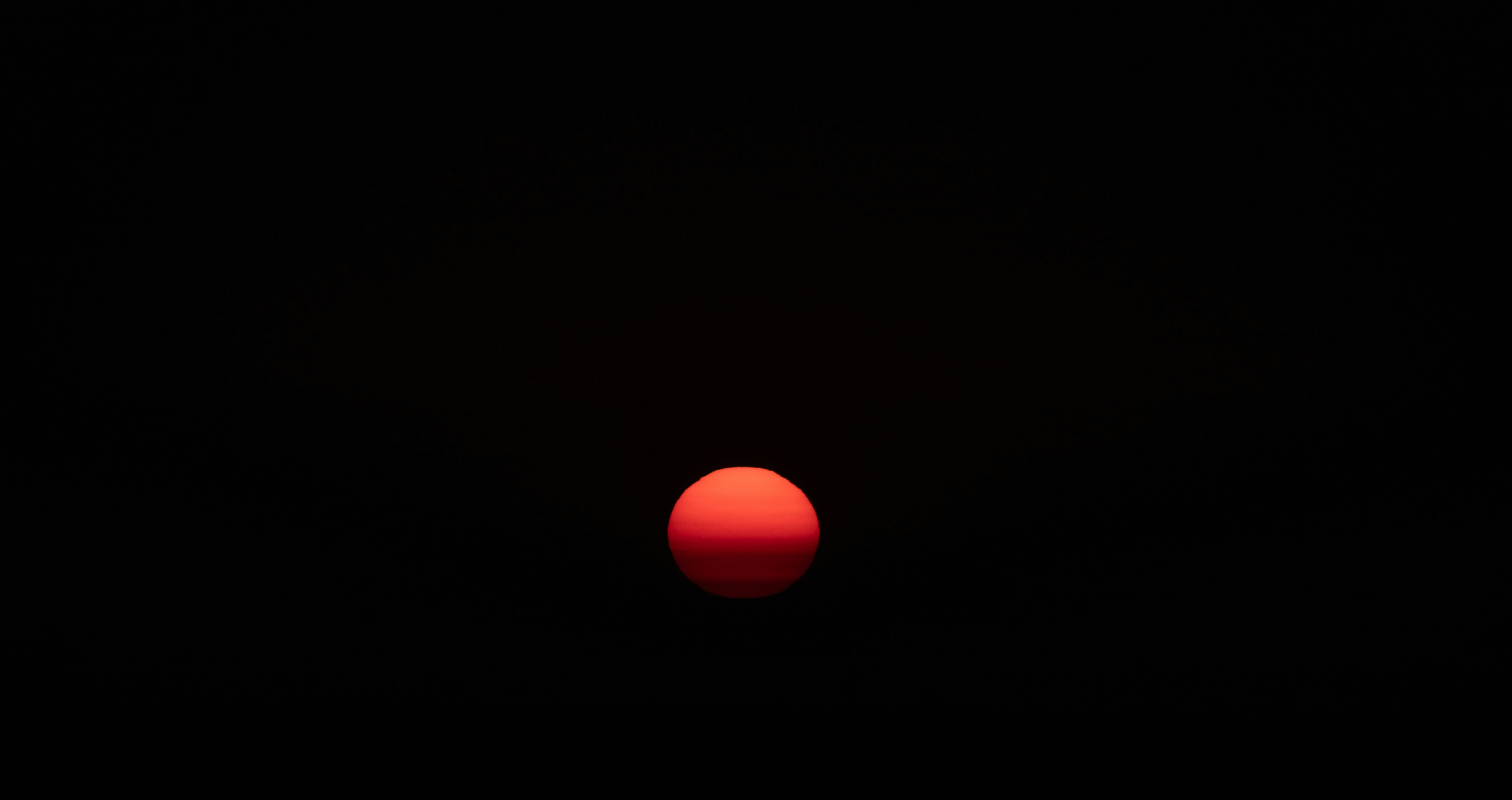 A vibrant red sun setting in a dark sky