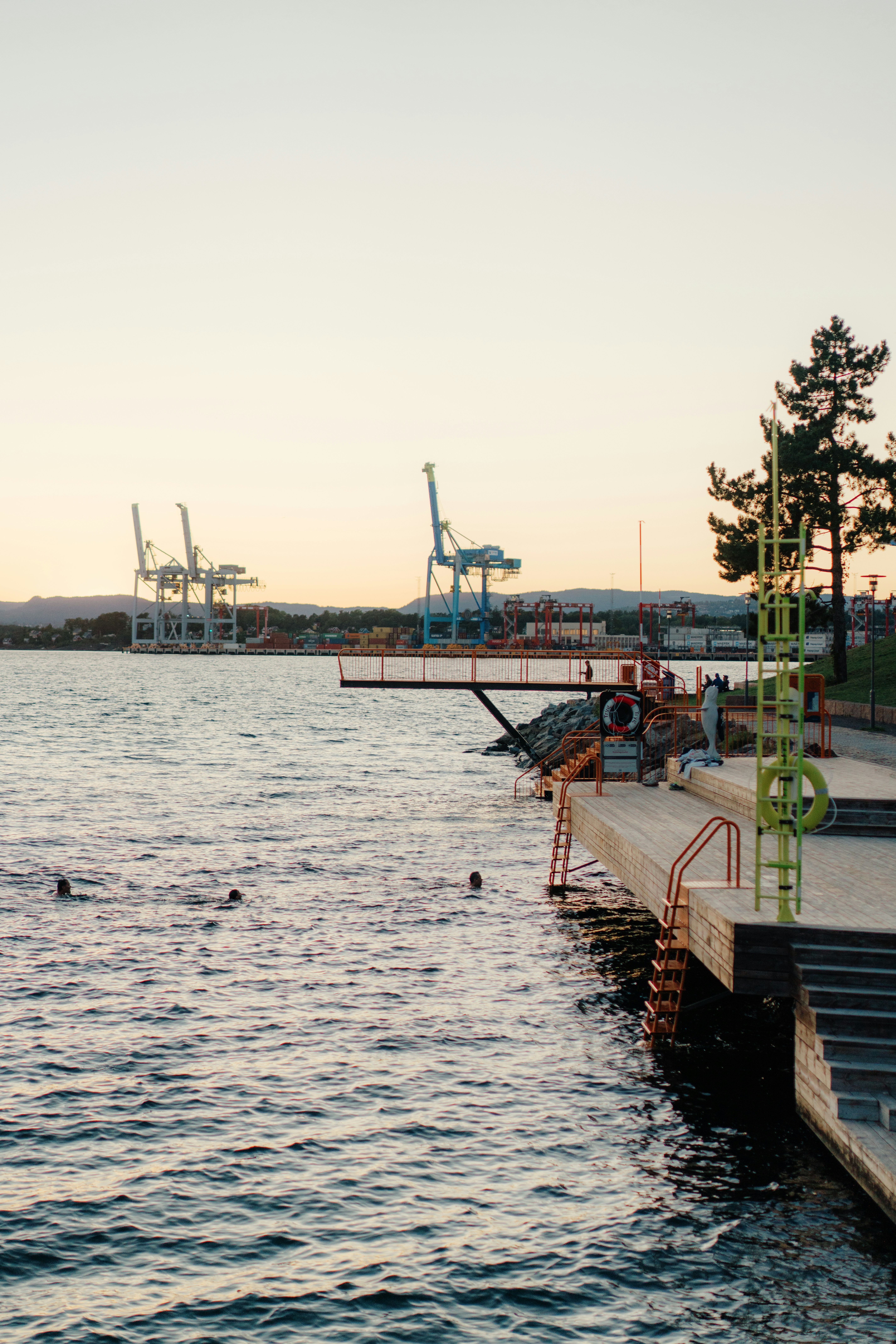 People swim near a modern pier at sunset
