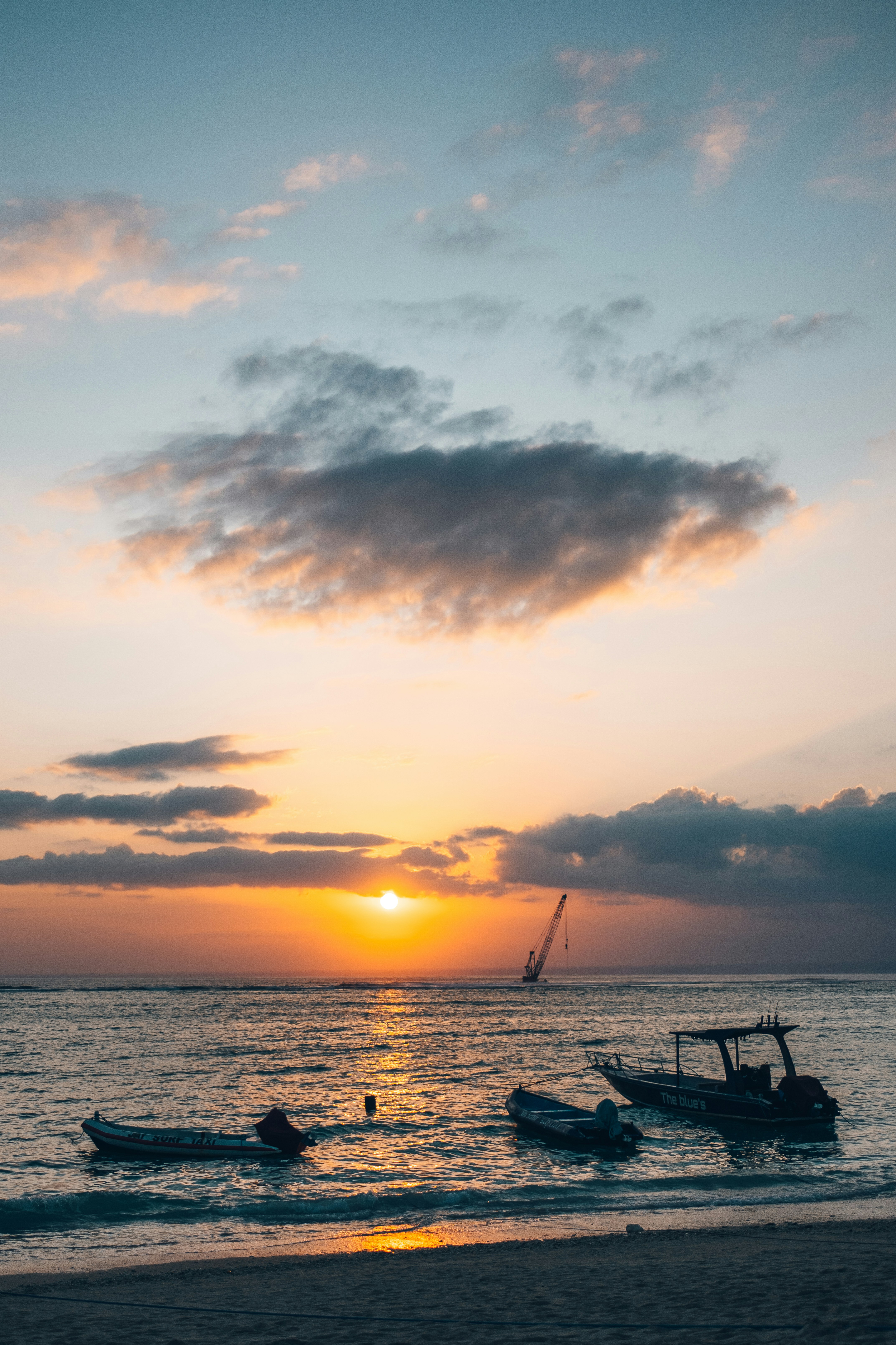 Boats on the ocean at sunset with colorful clouds.