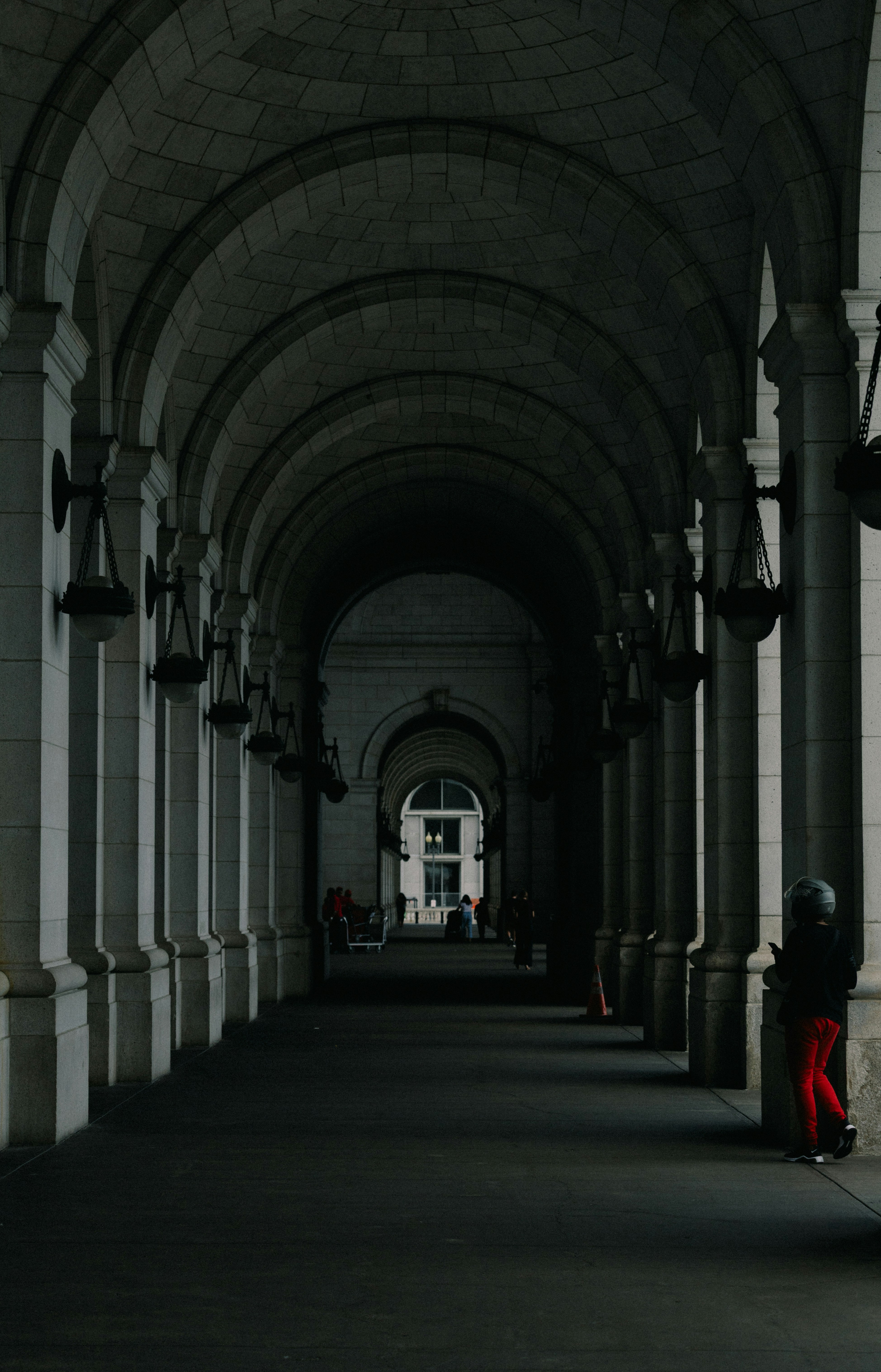 Person in red pants stands in arched stone hallway
