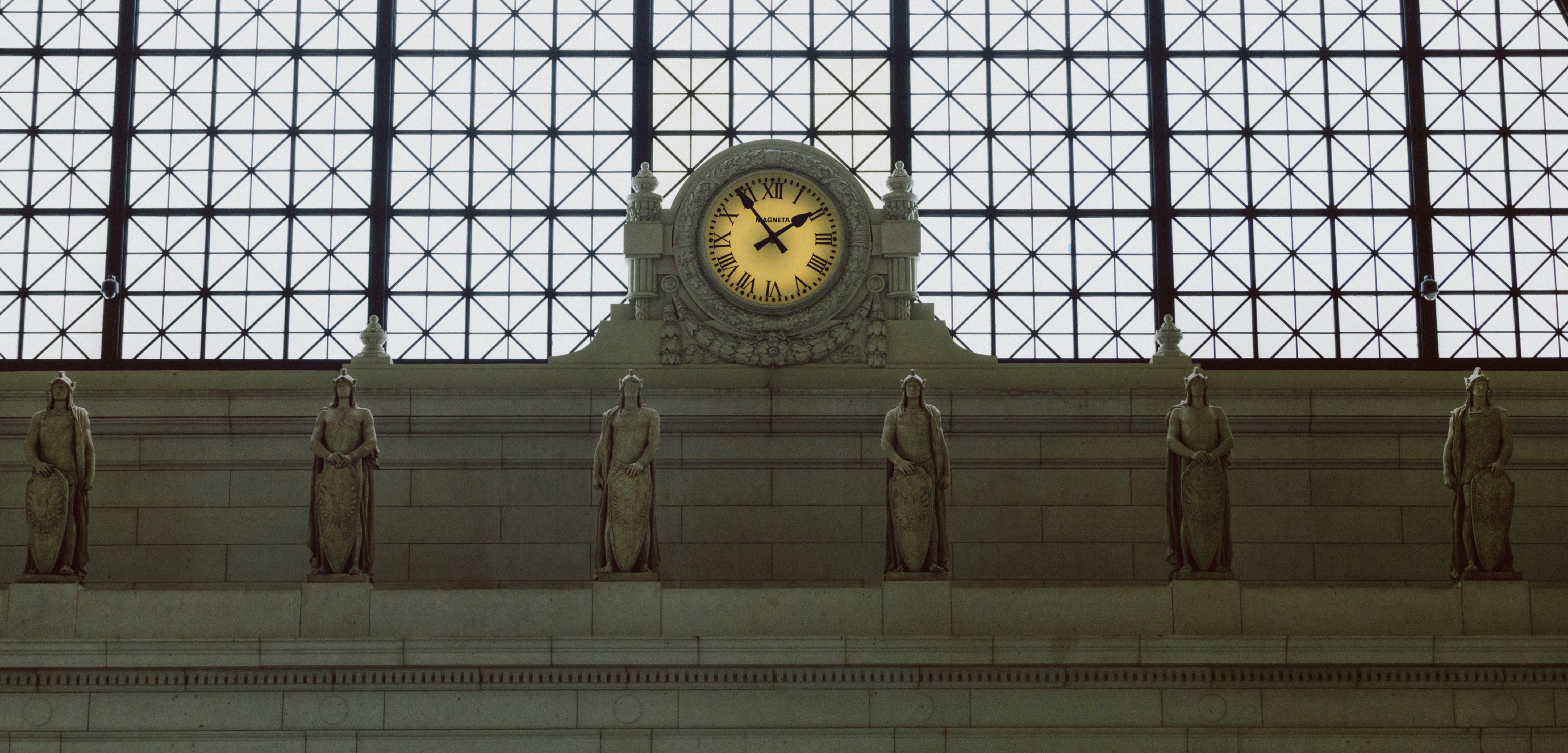 Ornate clock above statues under large window