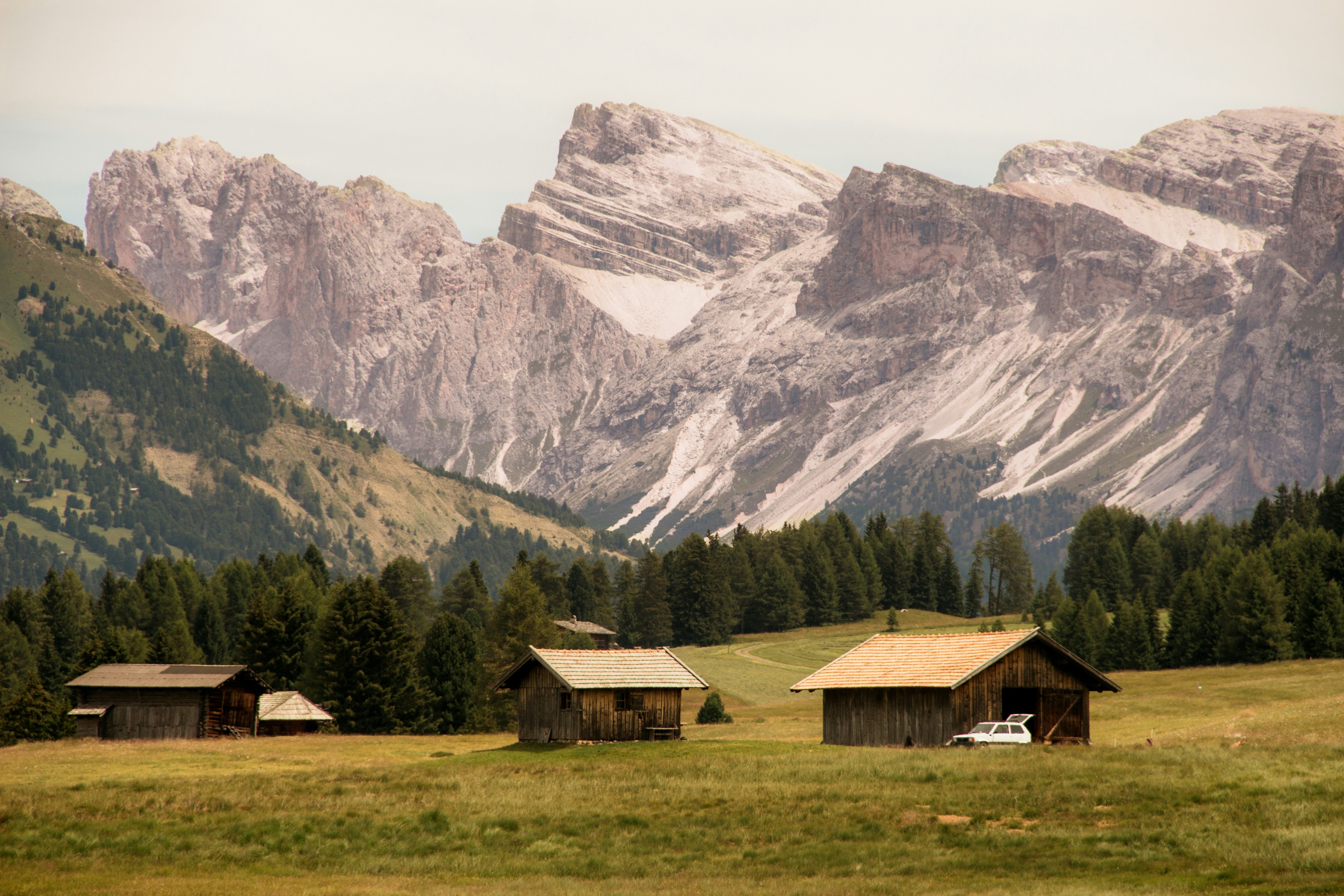 Seiser Alm in Italian Dolomites Alps | Wooden cabins in a grassy meadow with mountains behind.