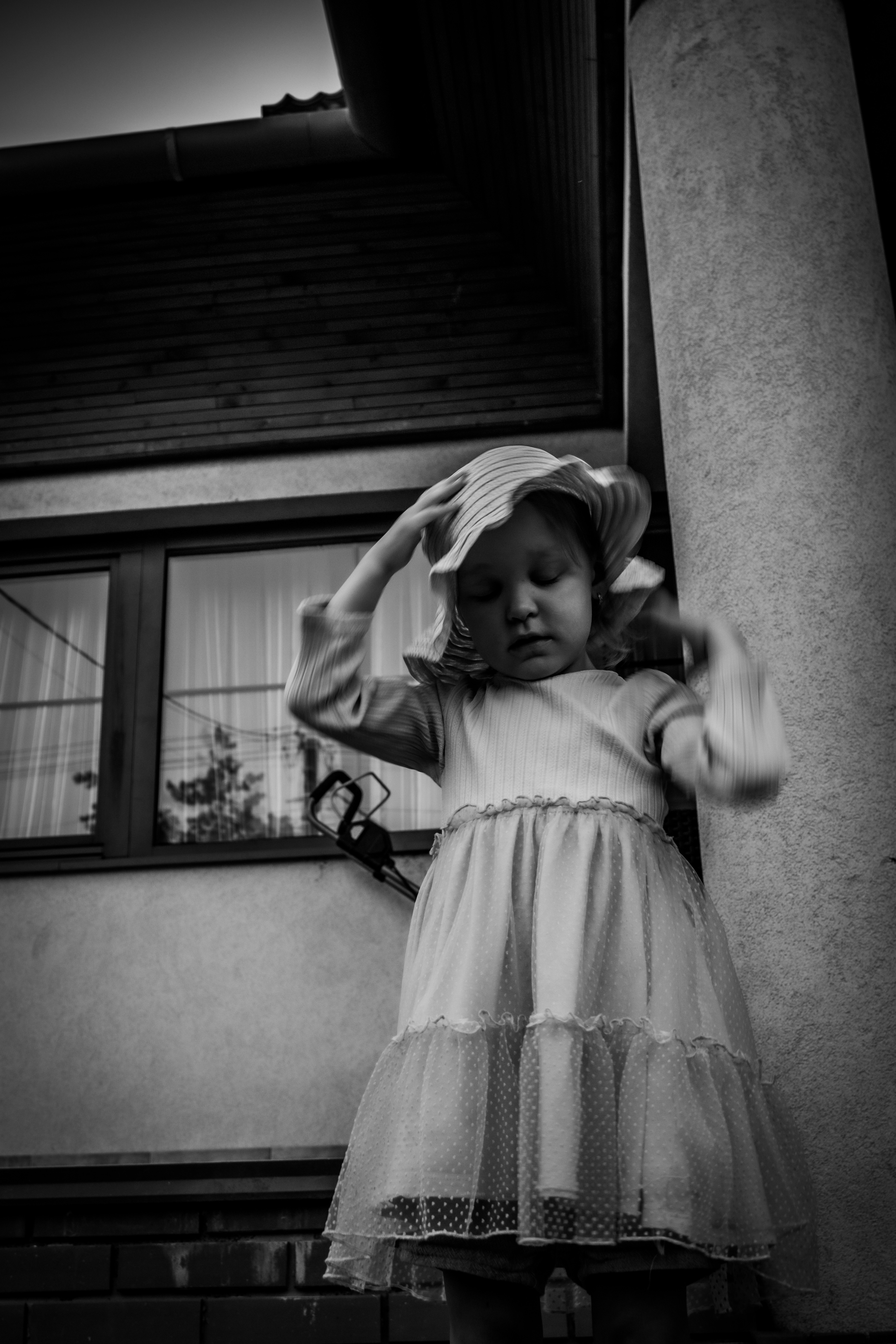 Young girl adjusting her hat by a column
