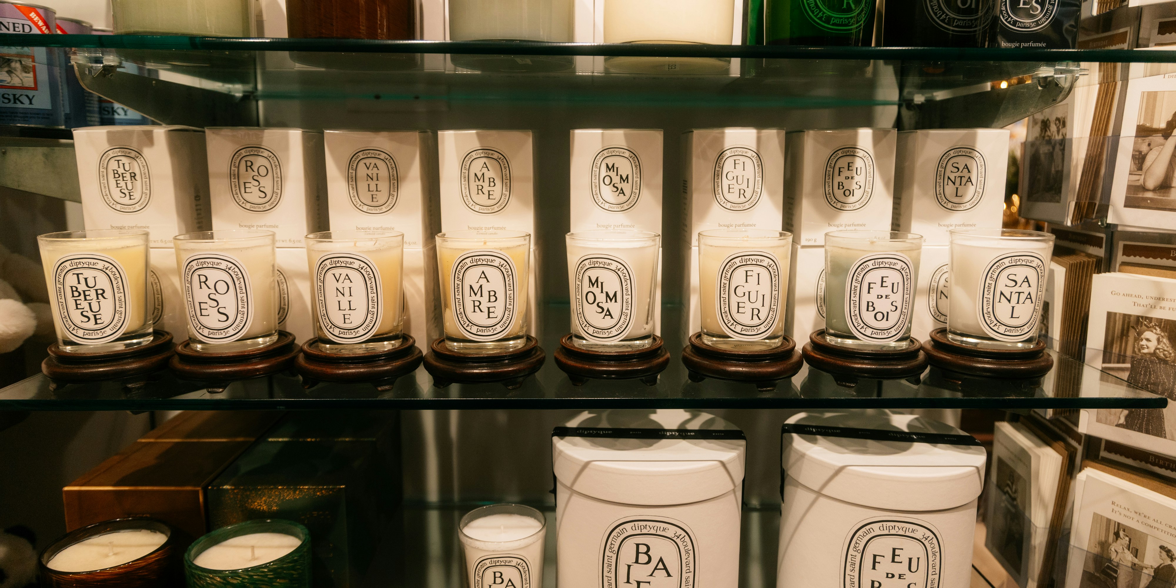 Elegant display of various scented candles arranged on glass shelves, showcasing distinct labels and designs that evoke a sense of luxury.