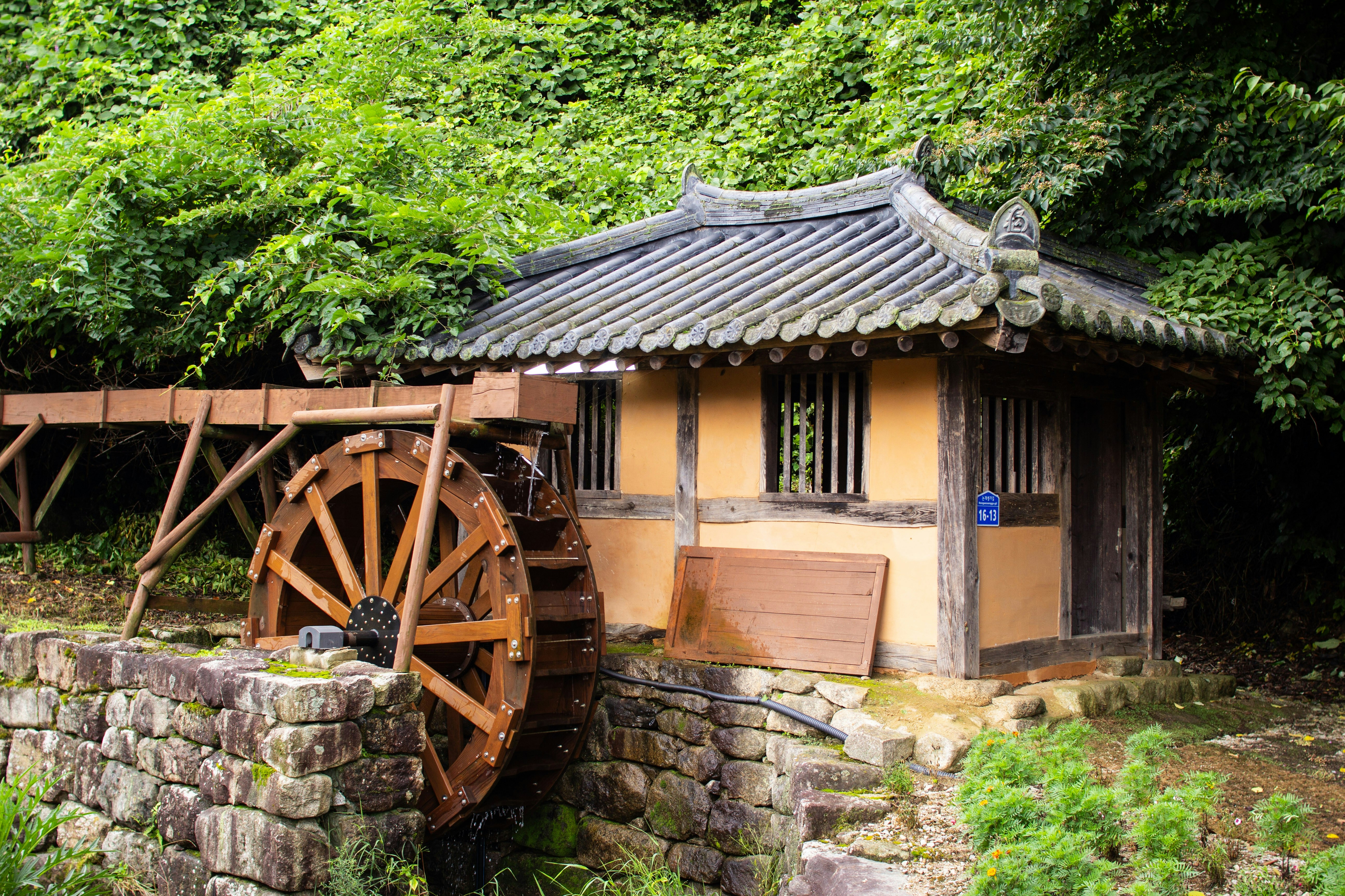 A traditional watermill nestled beside a stone wall, surrounded by lush greenery, showcasing the integration of architecture and nature.