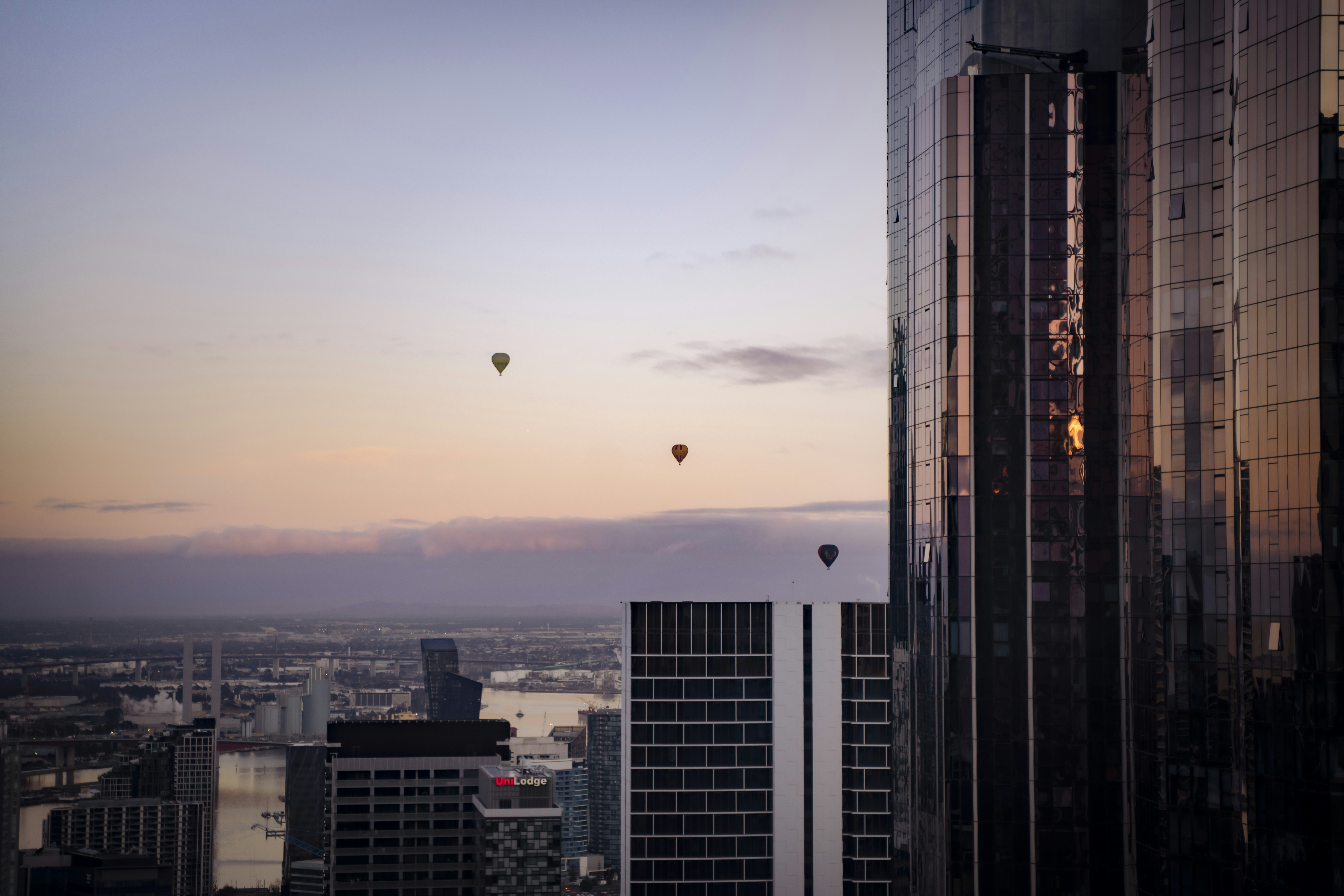 Hot air balloons float over city buildings at sunrise.
