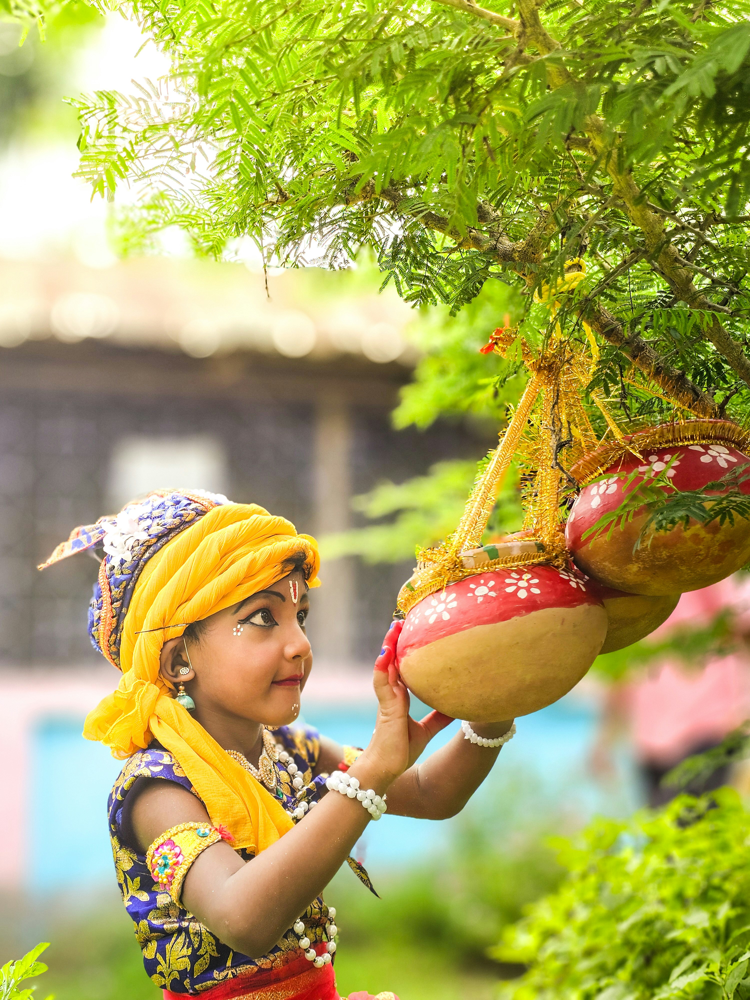 Child in vibrant traditional dress tends sacred pots under a sunlit tree