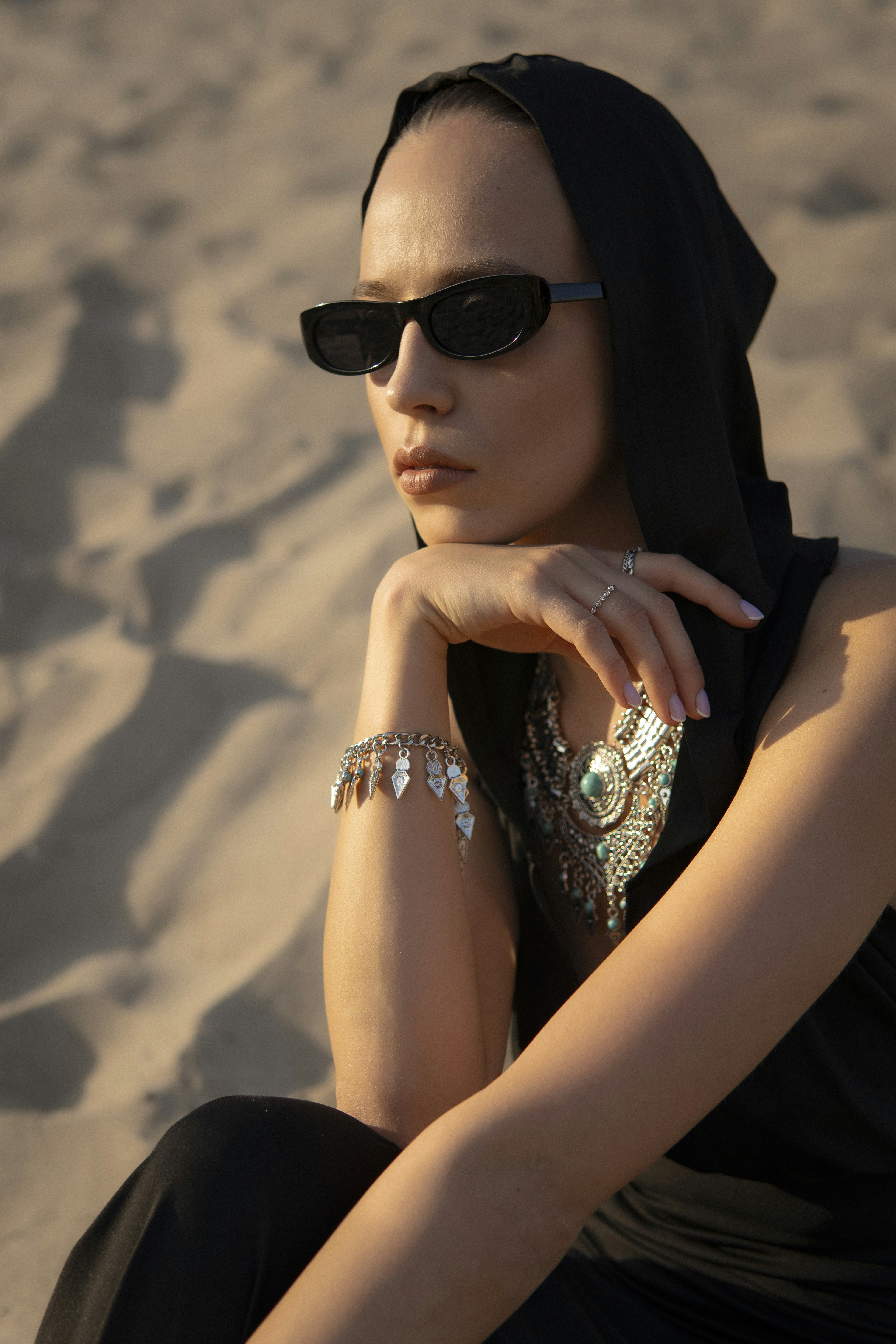Woman in sunglasses and black hood on sandy background
