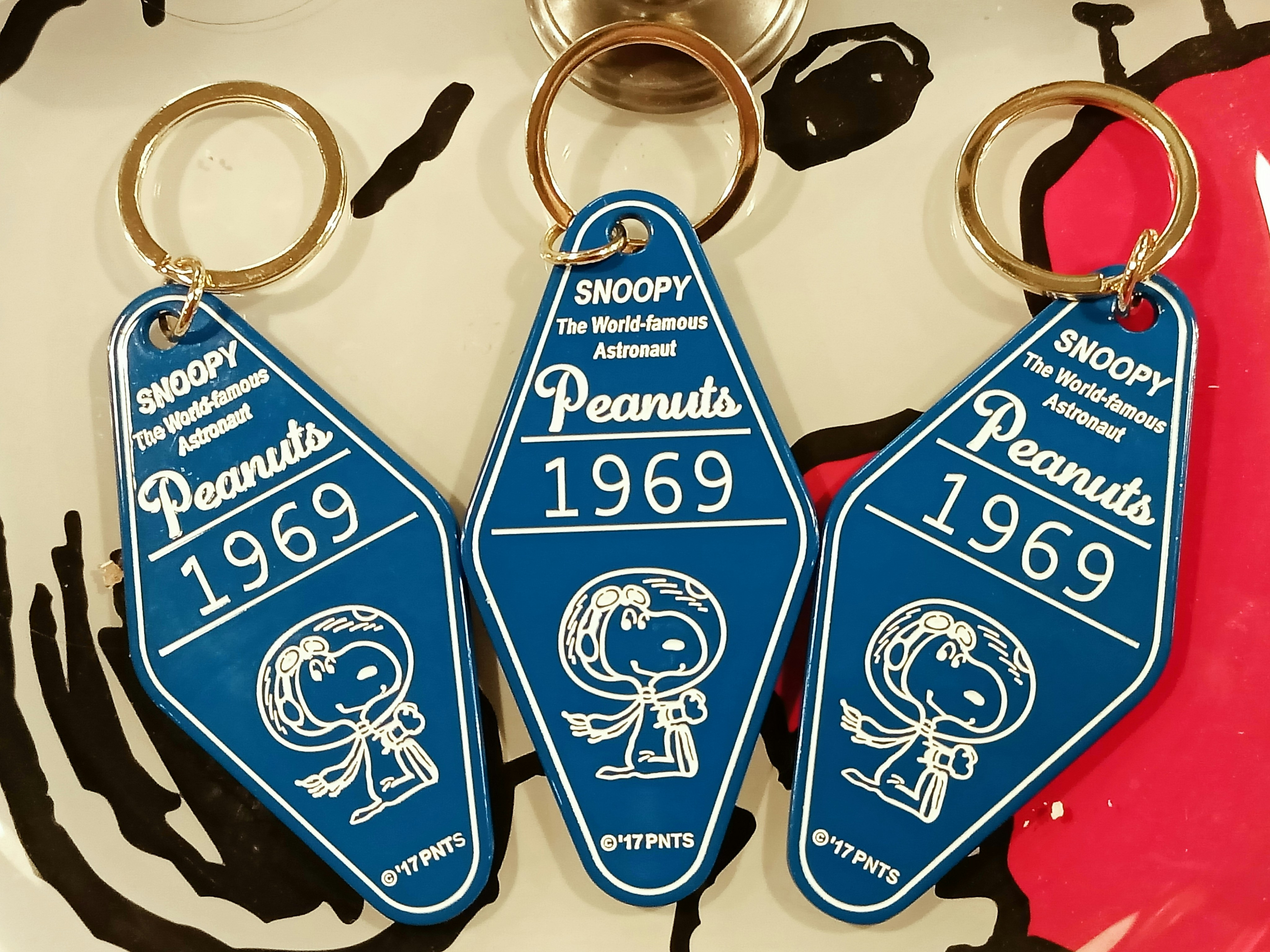 Three blue keychains featuring Snoopy, the Peanuts character, celebrating his role as the 'World-famous Astronaut' from 1969.