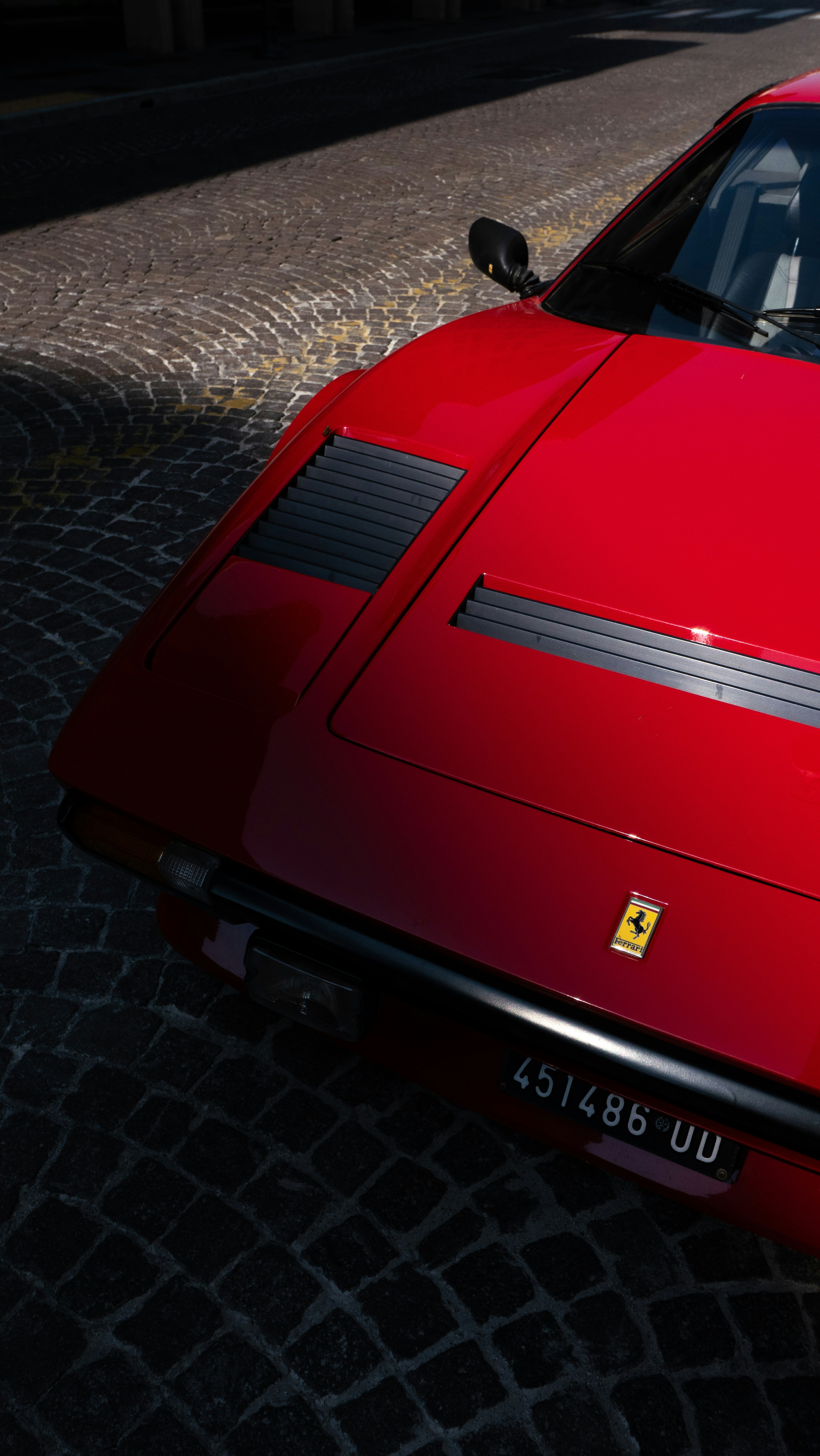 Close-up of a classic red Ferrari showcasing its sleek lines and iconic logo against a cobblestone backdrop.