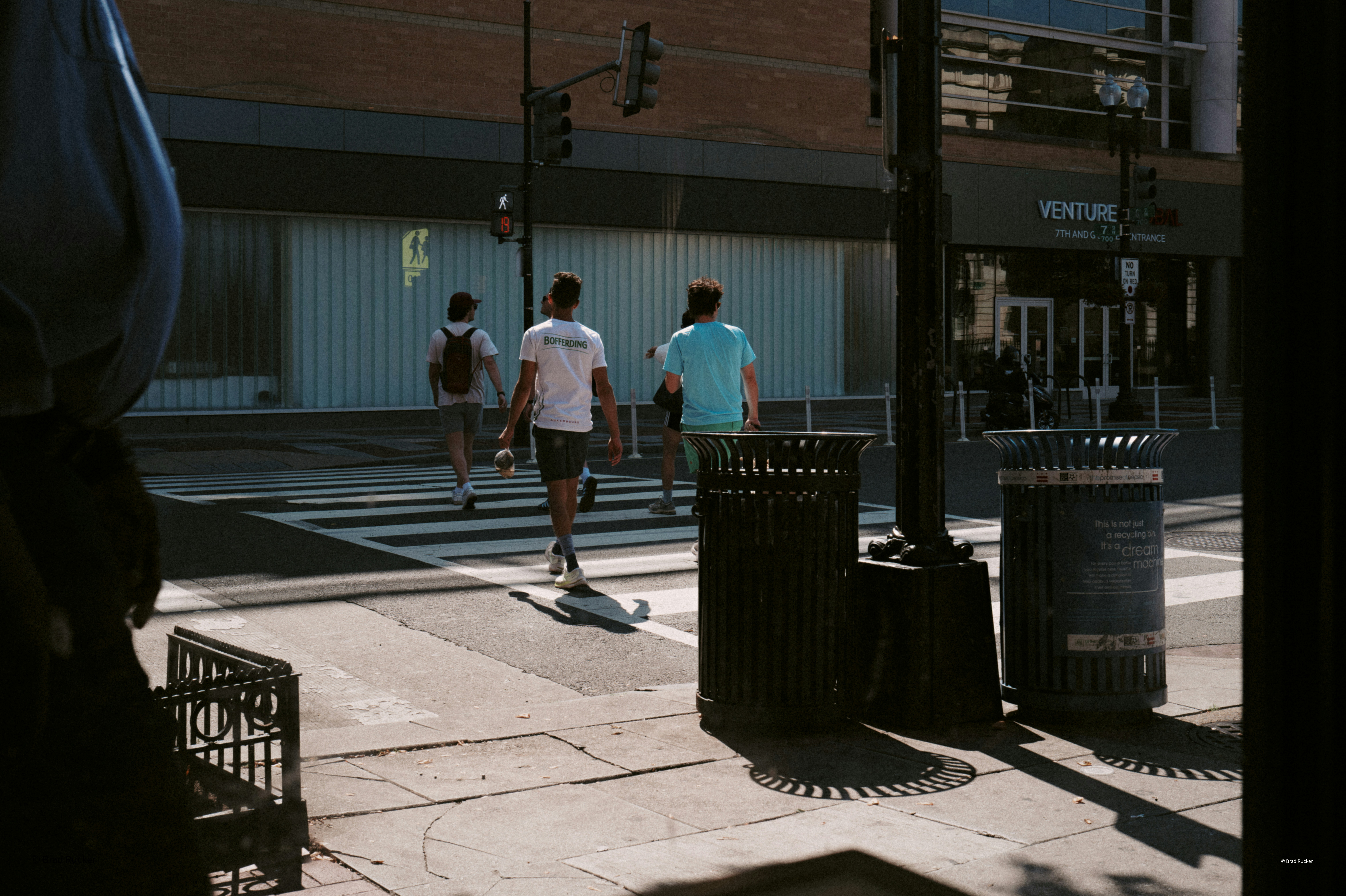 Three people cross a street on a skateboard.