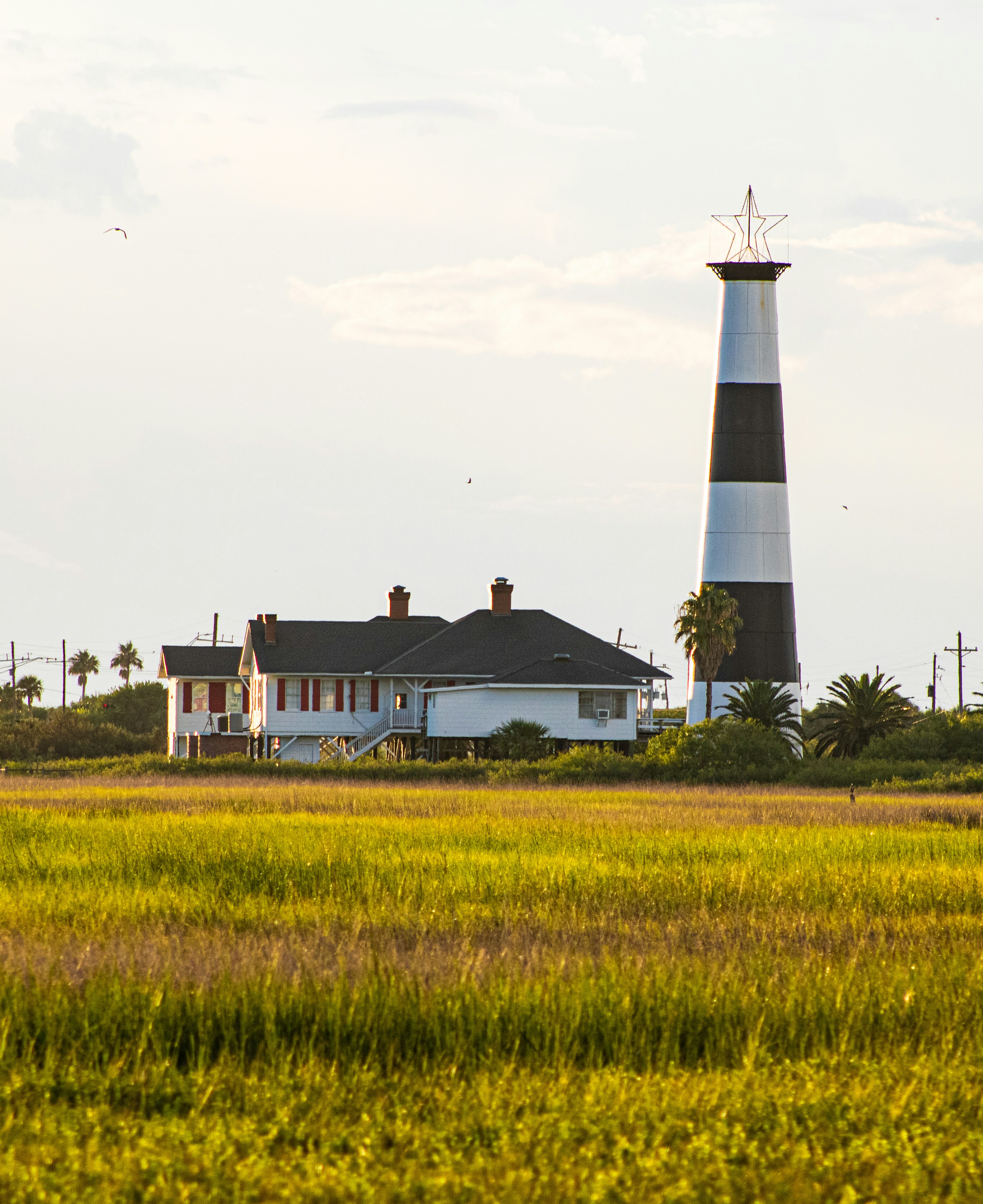 Point Bolivar Lighthouse at Bolivar Peninsula | Striped lighthouse with coastal buildings and marshland.