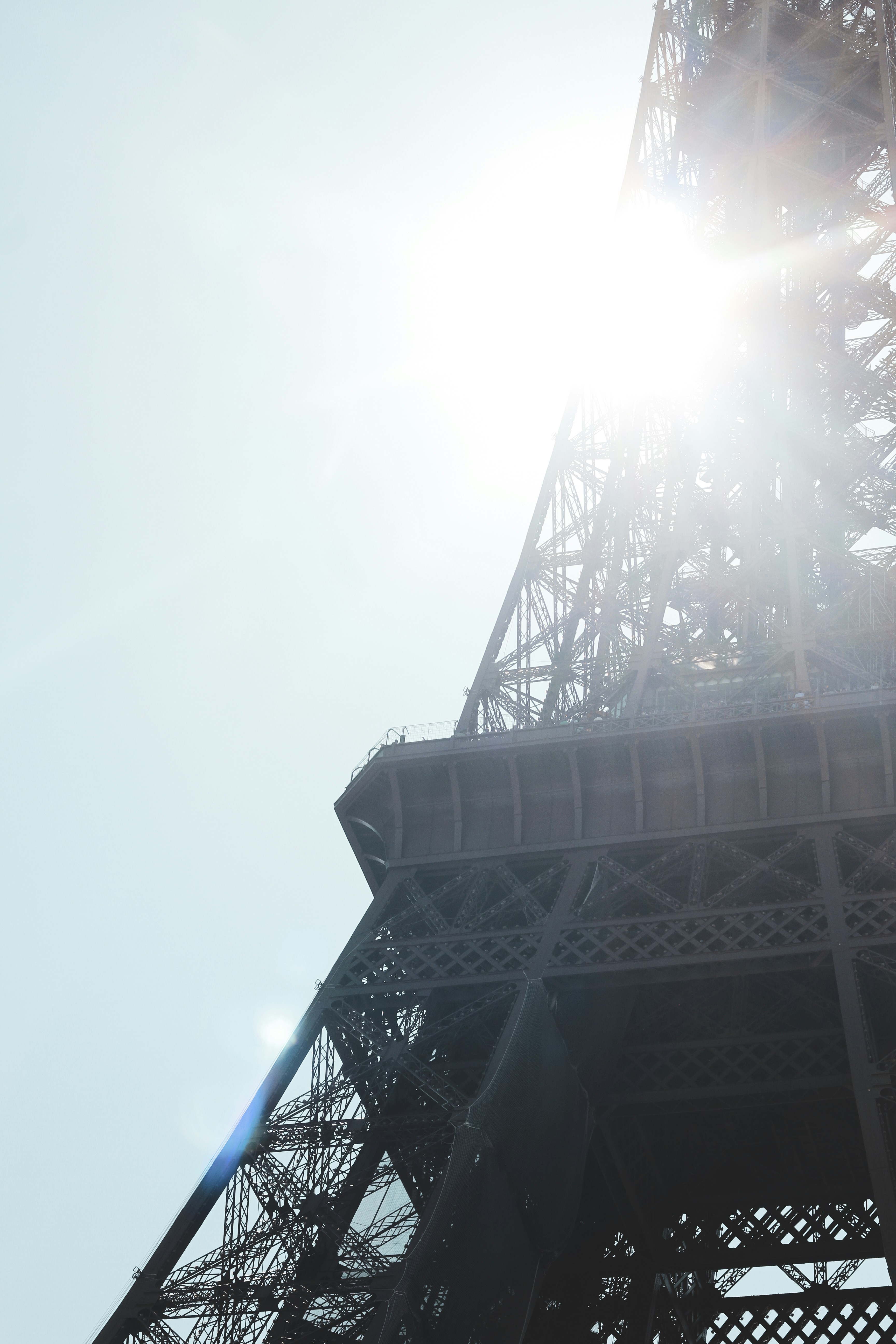 Sunlight streaming through the intricate ironwork of the Eiffel Tower, highlighting its architectural beauty against a clear sky.