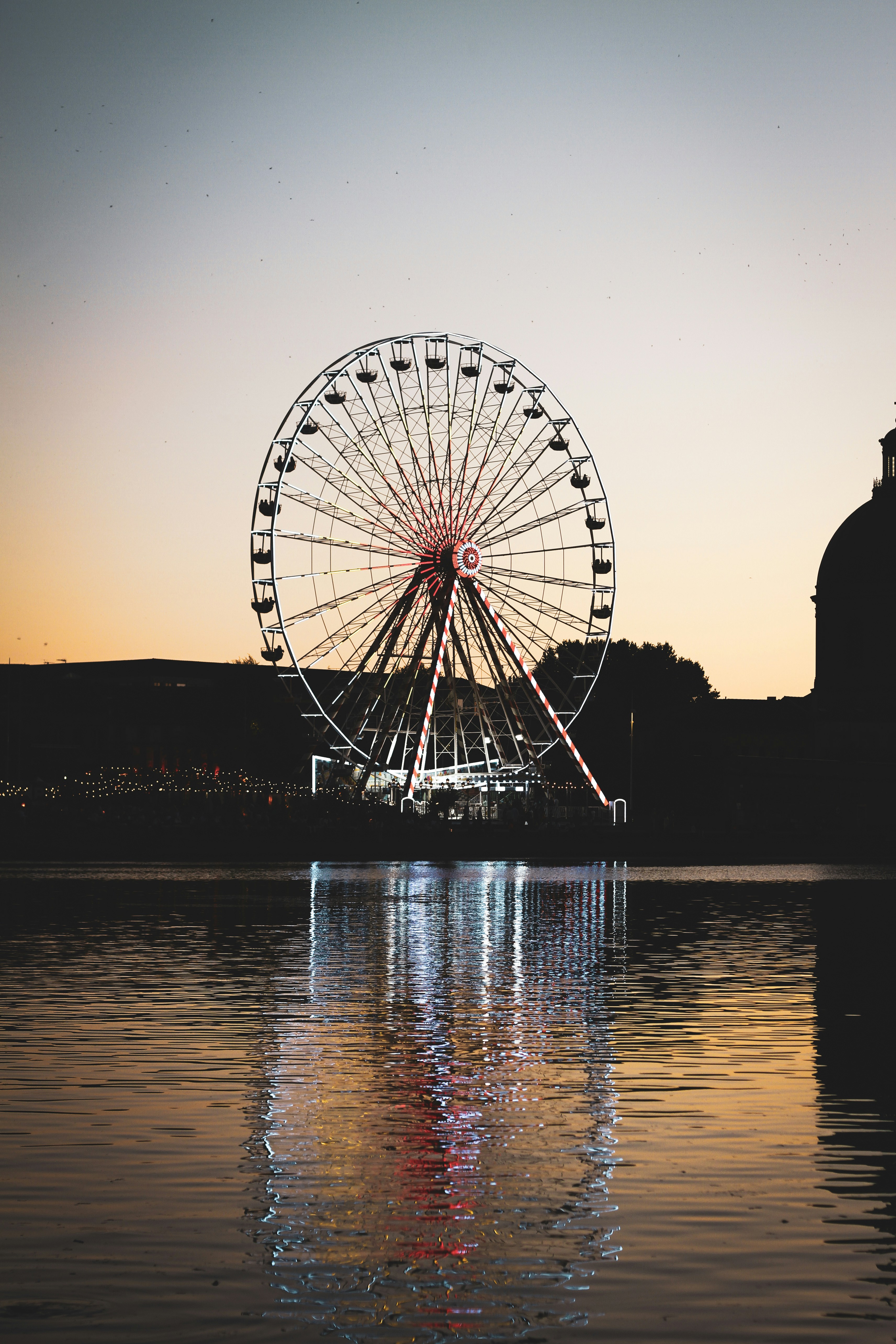 Ferris wheel illuminated against a twilight sky, mirrored in the calm waters below.