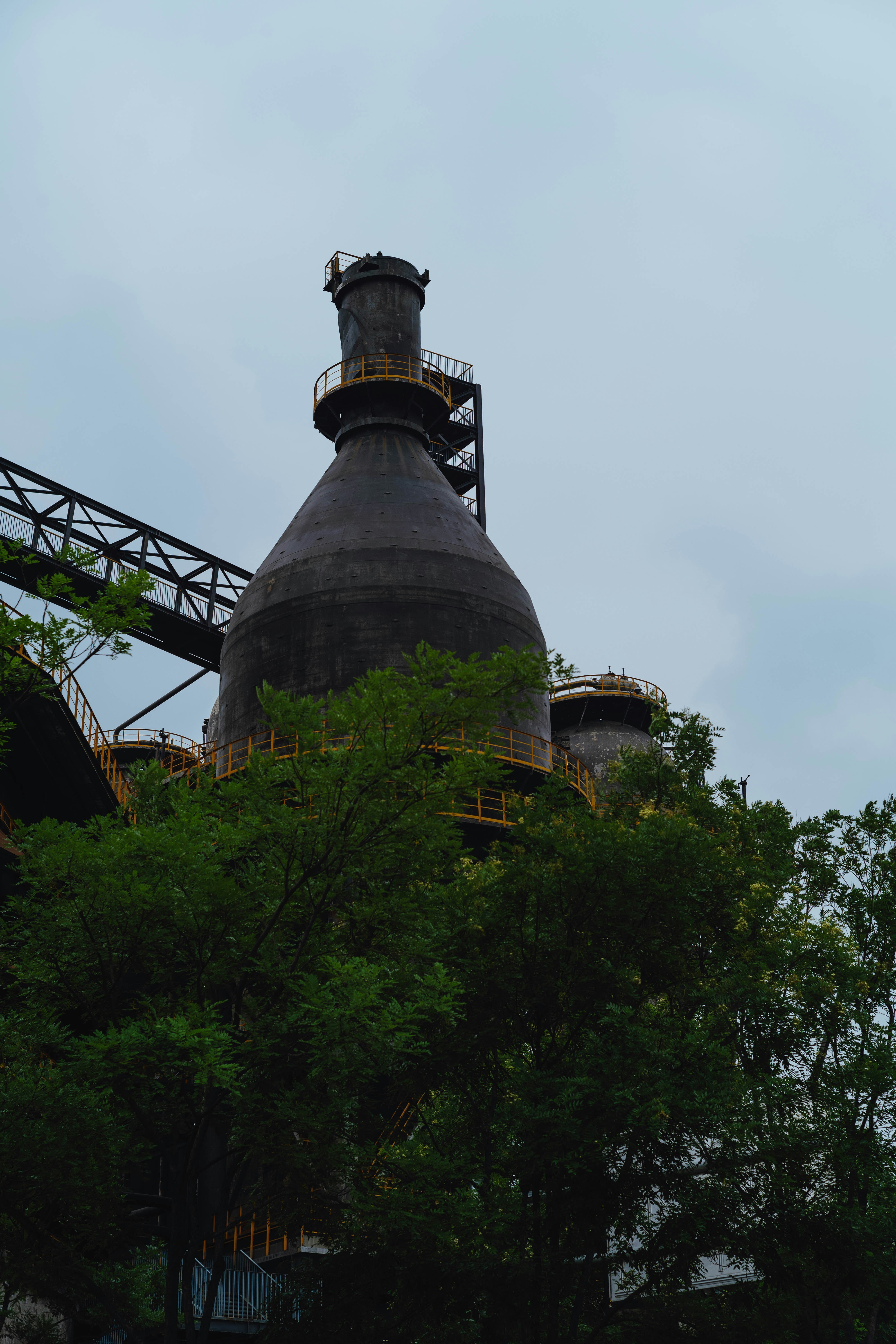 An imposing industrial structure rises amidst lush greenery, showcasing the intersection of nature and machinery. The scene captures a blend of history and modernity.