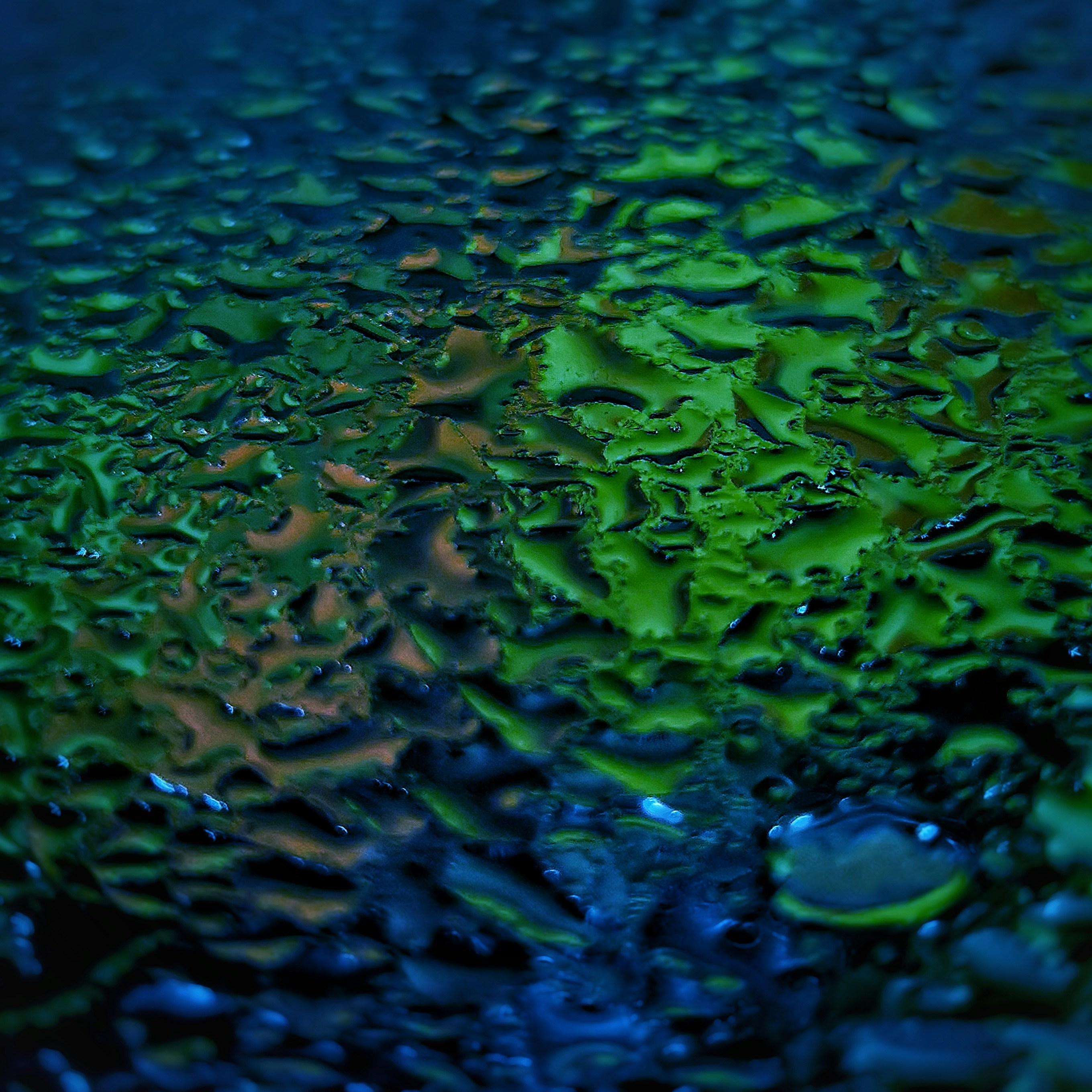 Close-up of water droplets on a surface with green and blue hues