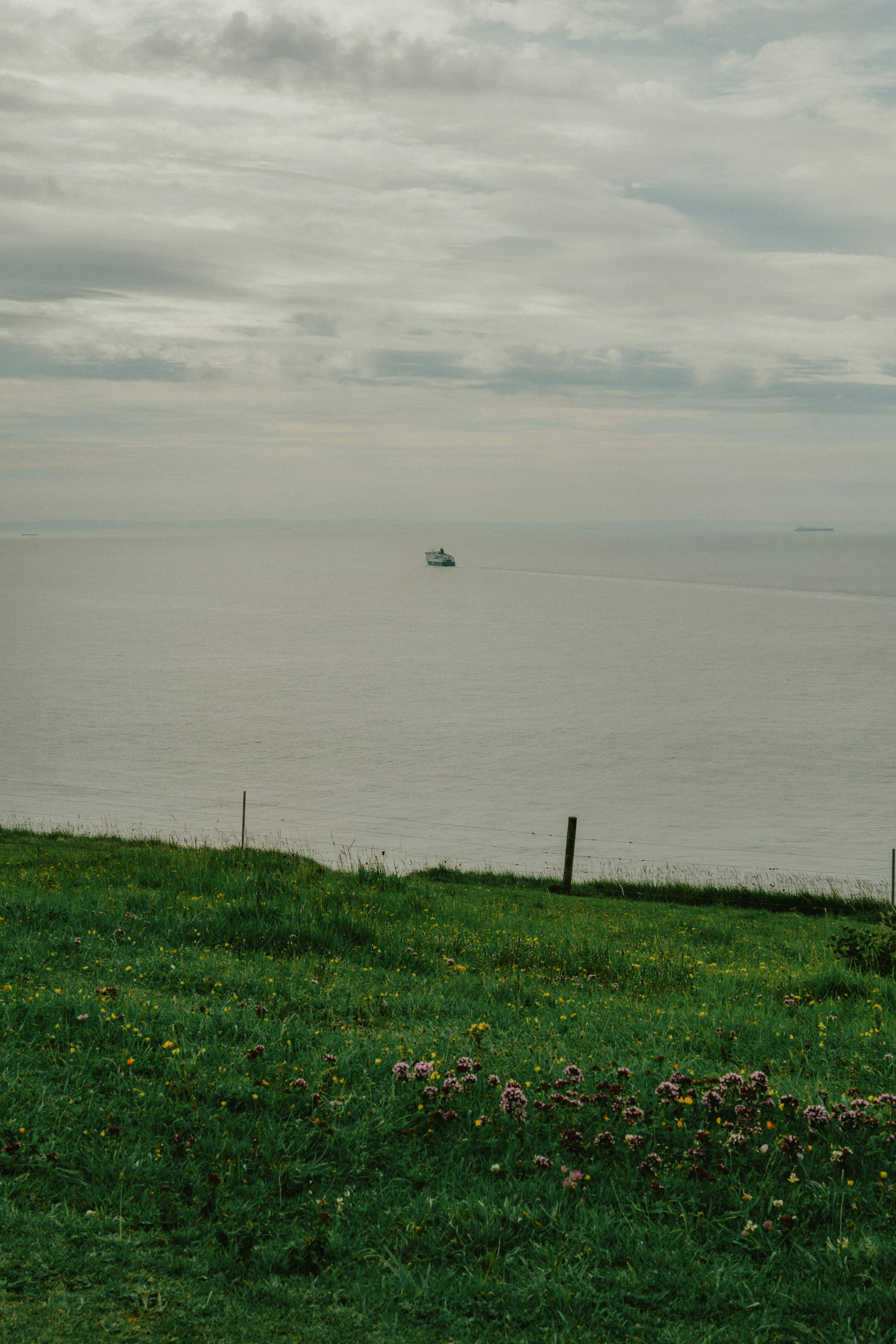 A lone ship sails on a hazy ocean undercast sea.