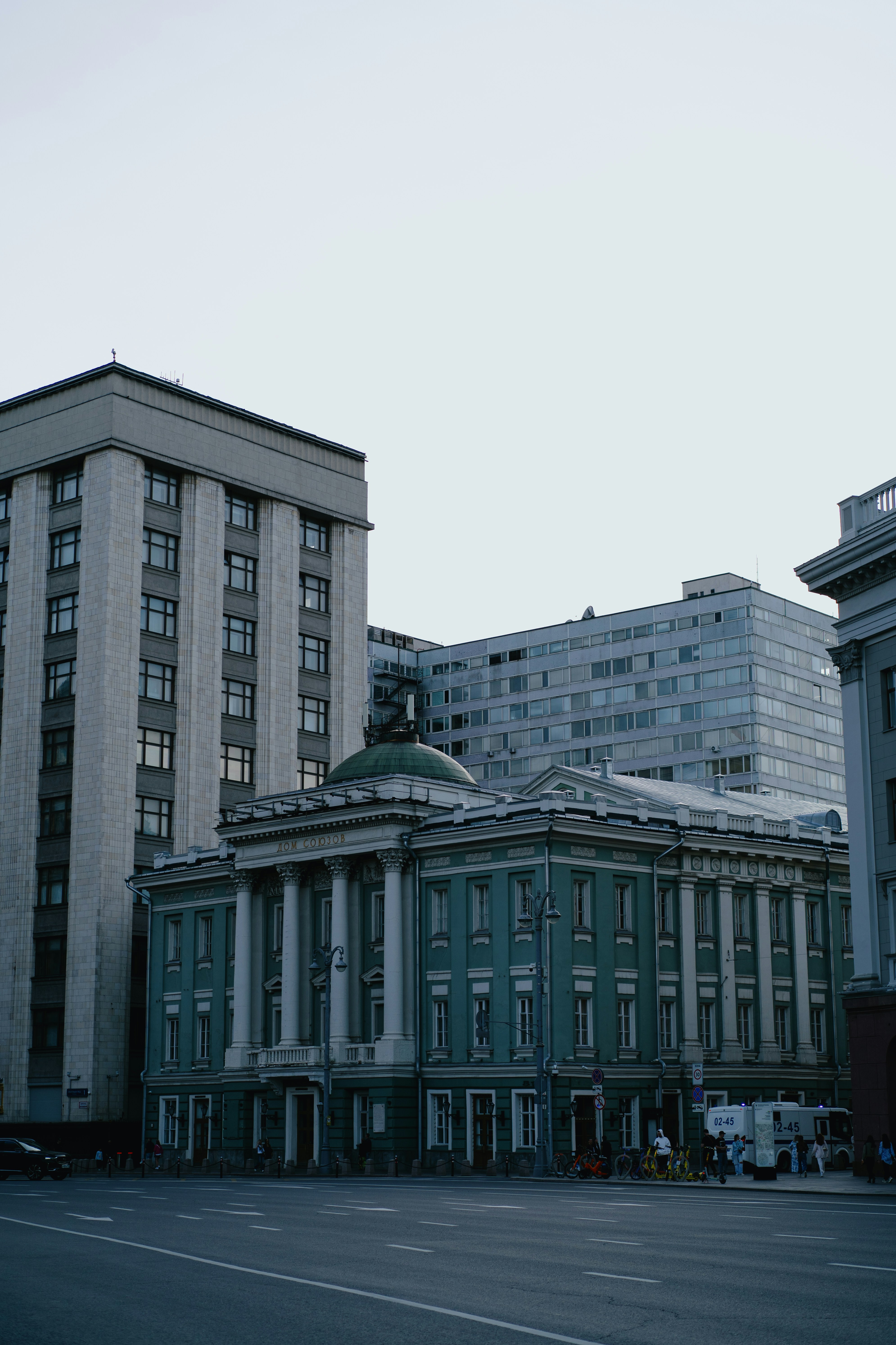 Historic teal building with columns and modern structures
