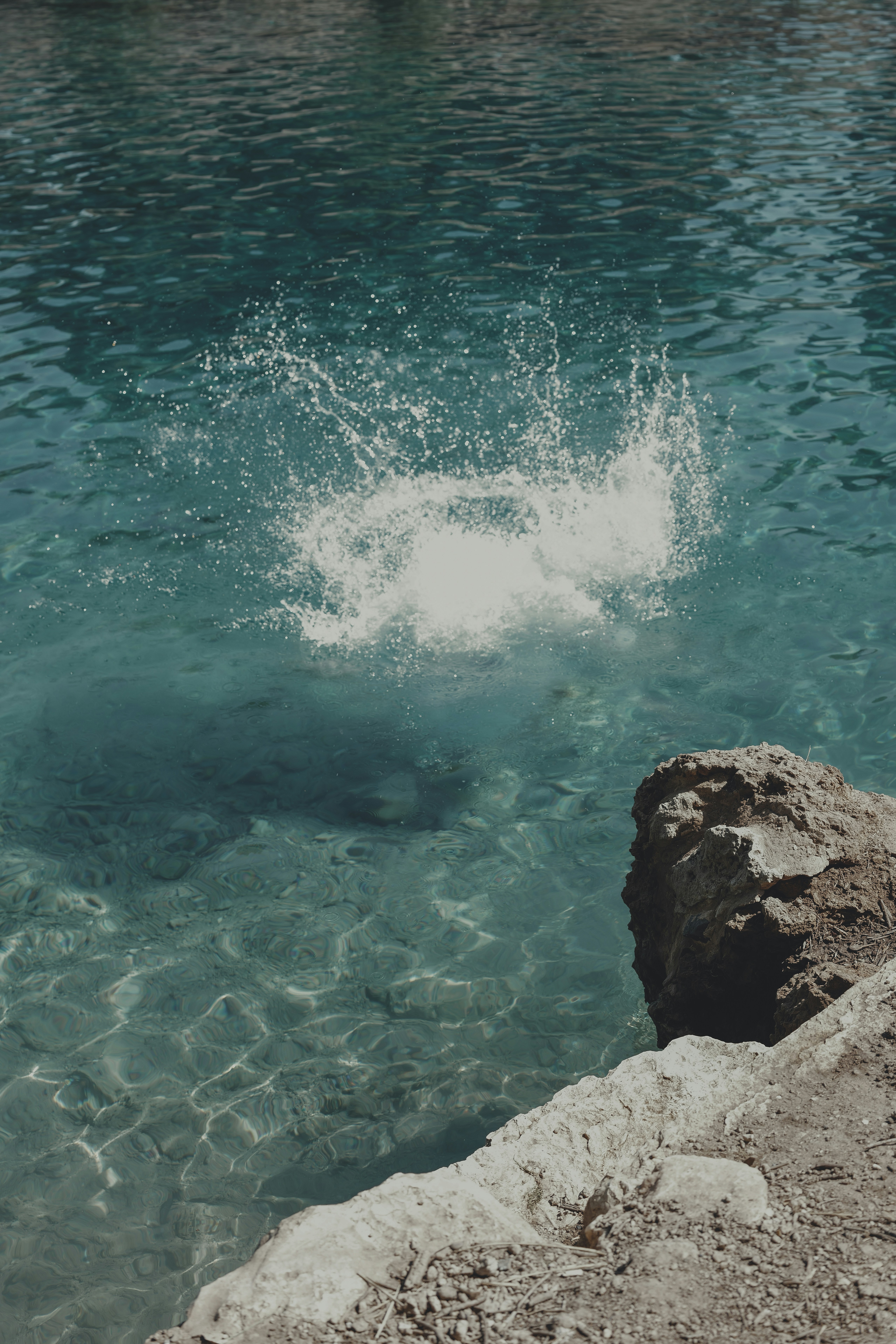 A dramatic splash in crystal-clear water, captured mid-jump. A moment of energy contrasting a calm scene. | Person jumping into clear turquoise water creating splash.