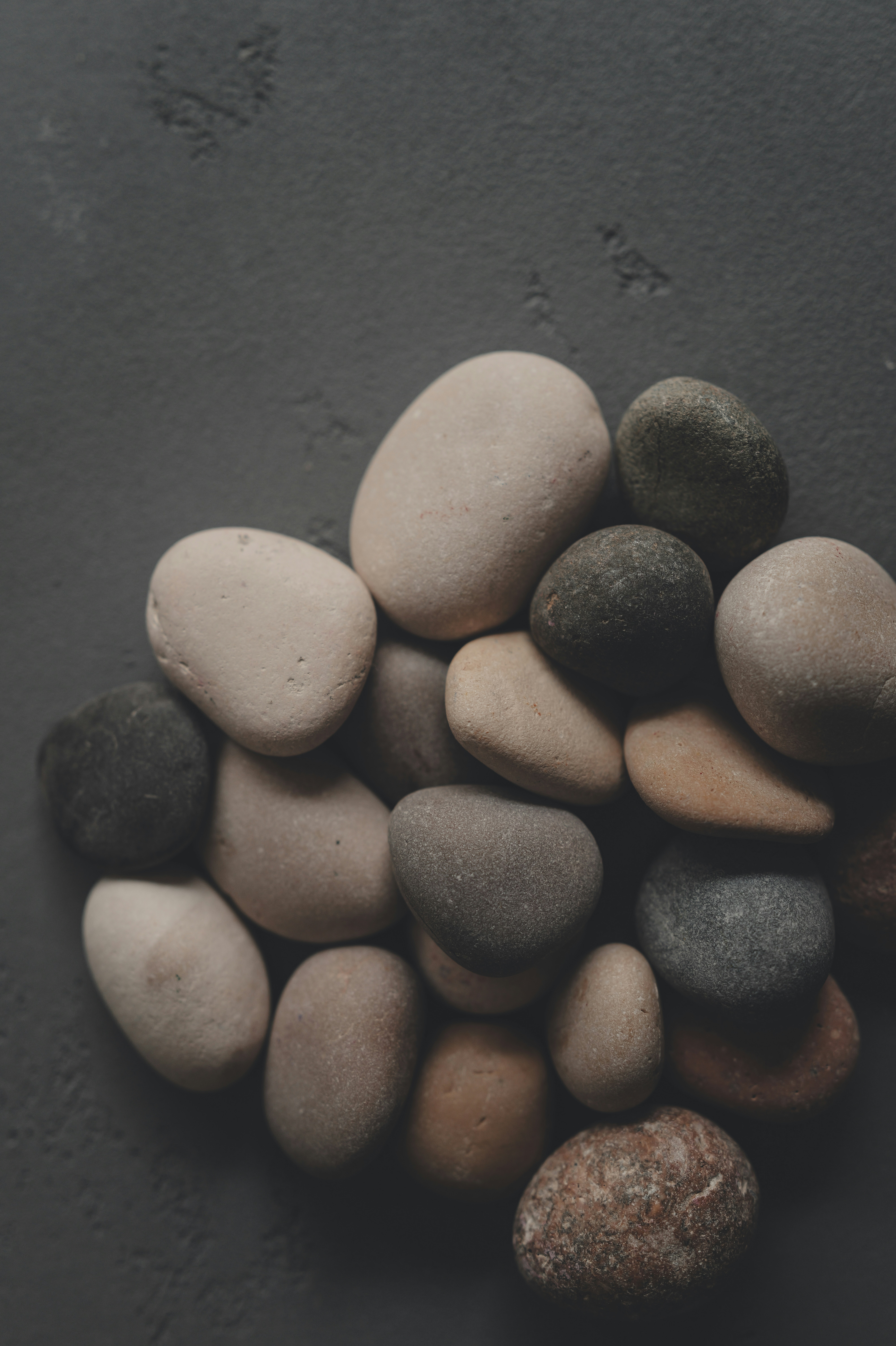 A collection of smooth, rounded stones arranged on a dark surface, showcasing a variety of earthy tones and textures.