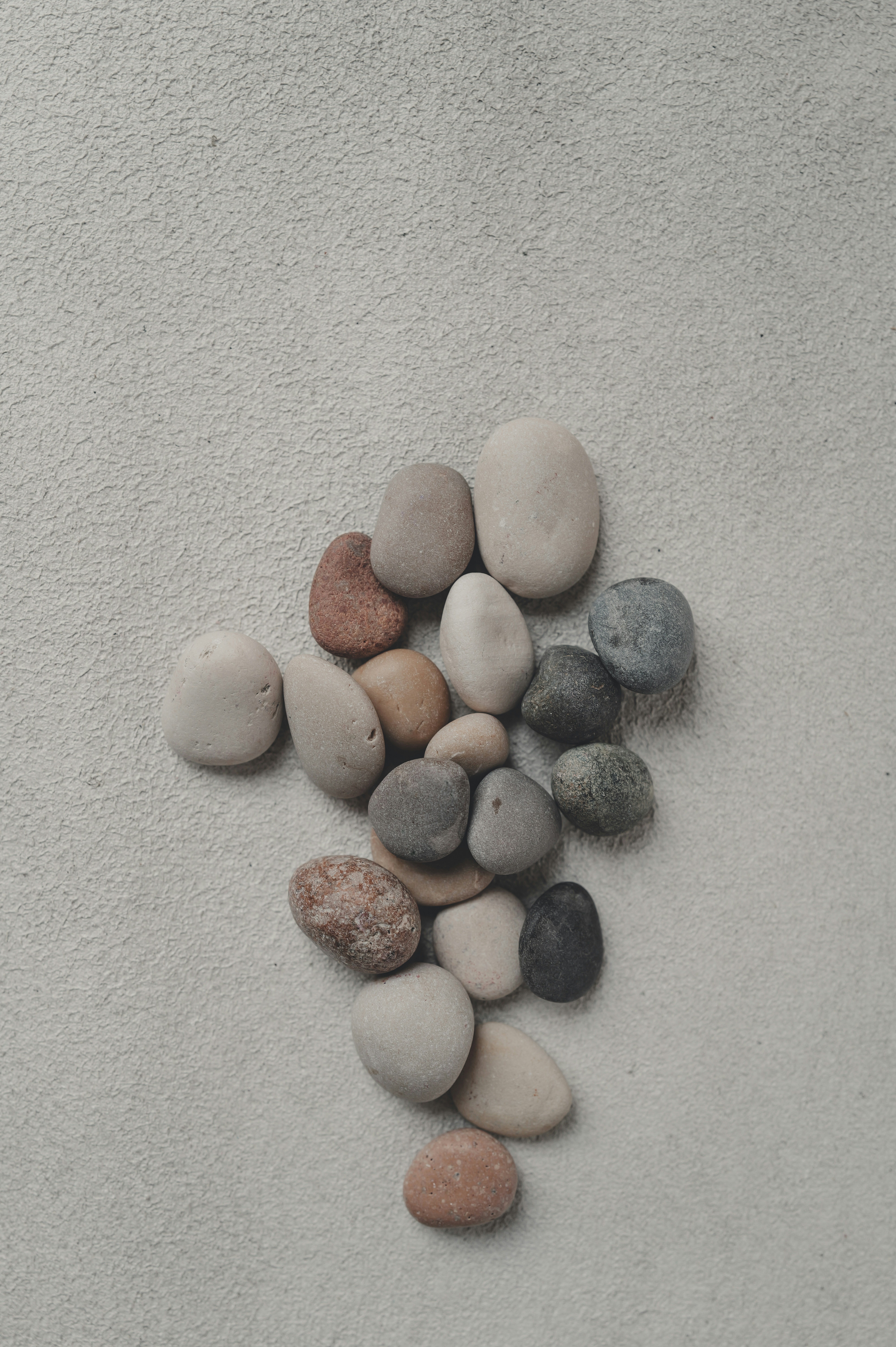 Natural pebbles scattered on a textured light surface. A soft, organic composition with muted tones. | A collection of smooth, varied stones on sand