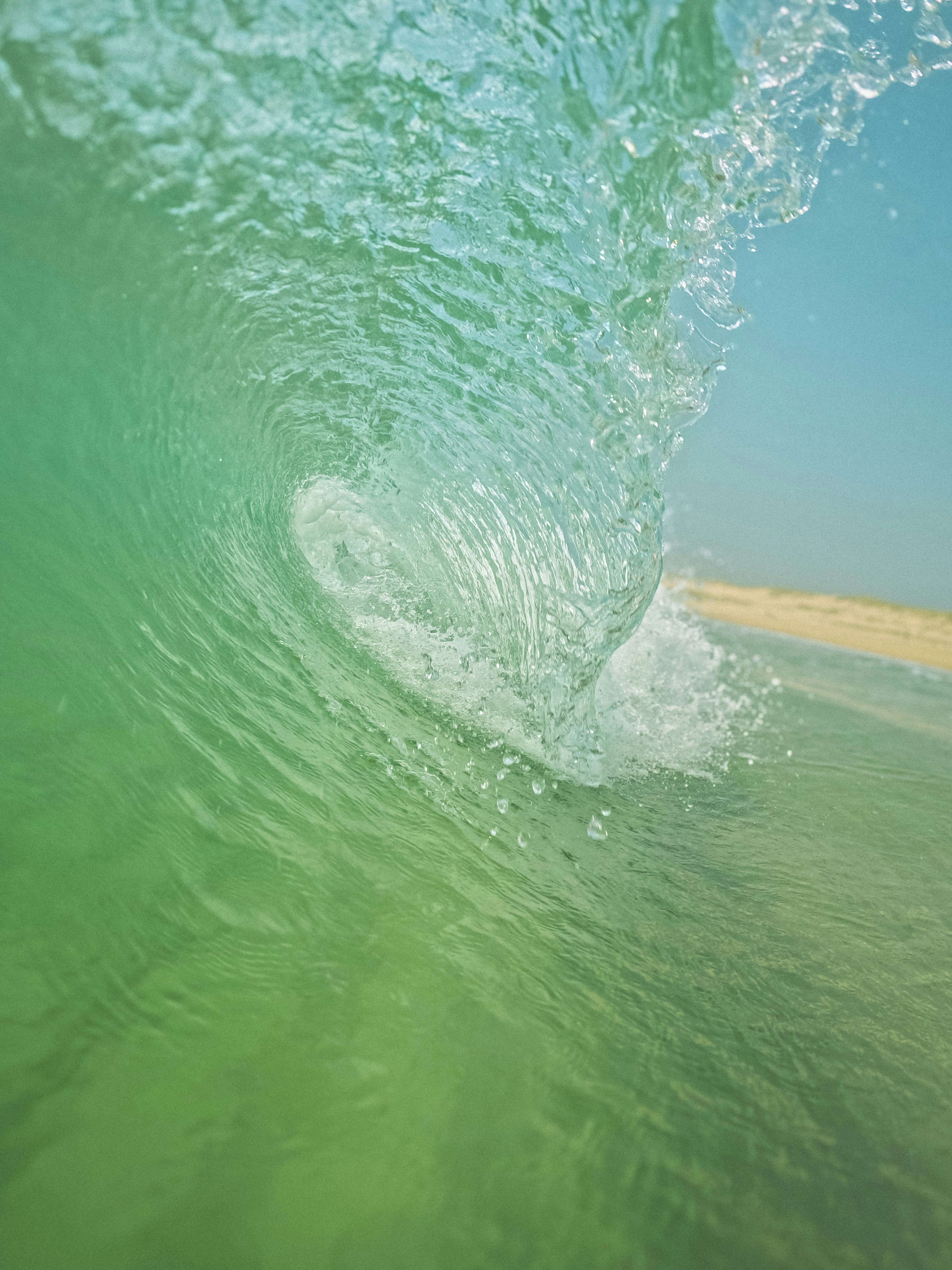 Translucent wave curling over the shoreline, capturing the essence of ocean motion and light play. The scene highlights the dynamic interaction between water and sand.