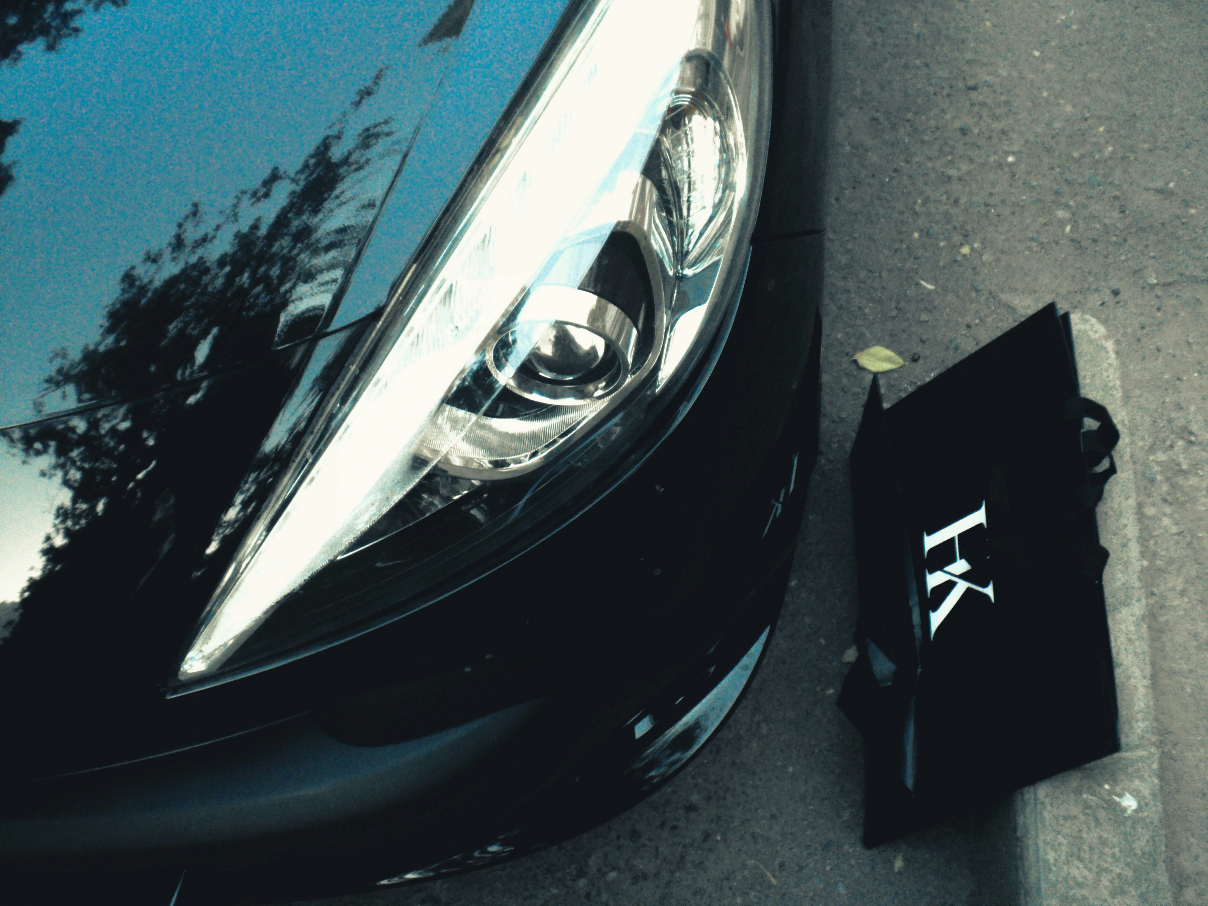 The beautiful tension between sleek design and rough reality. | Black car parked next to a curb with bag