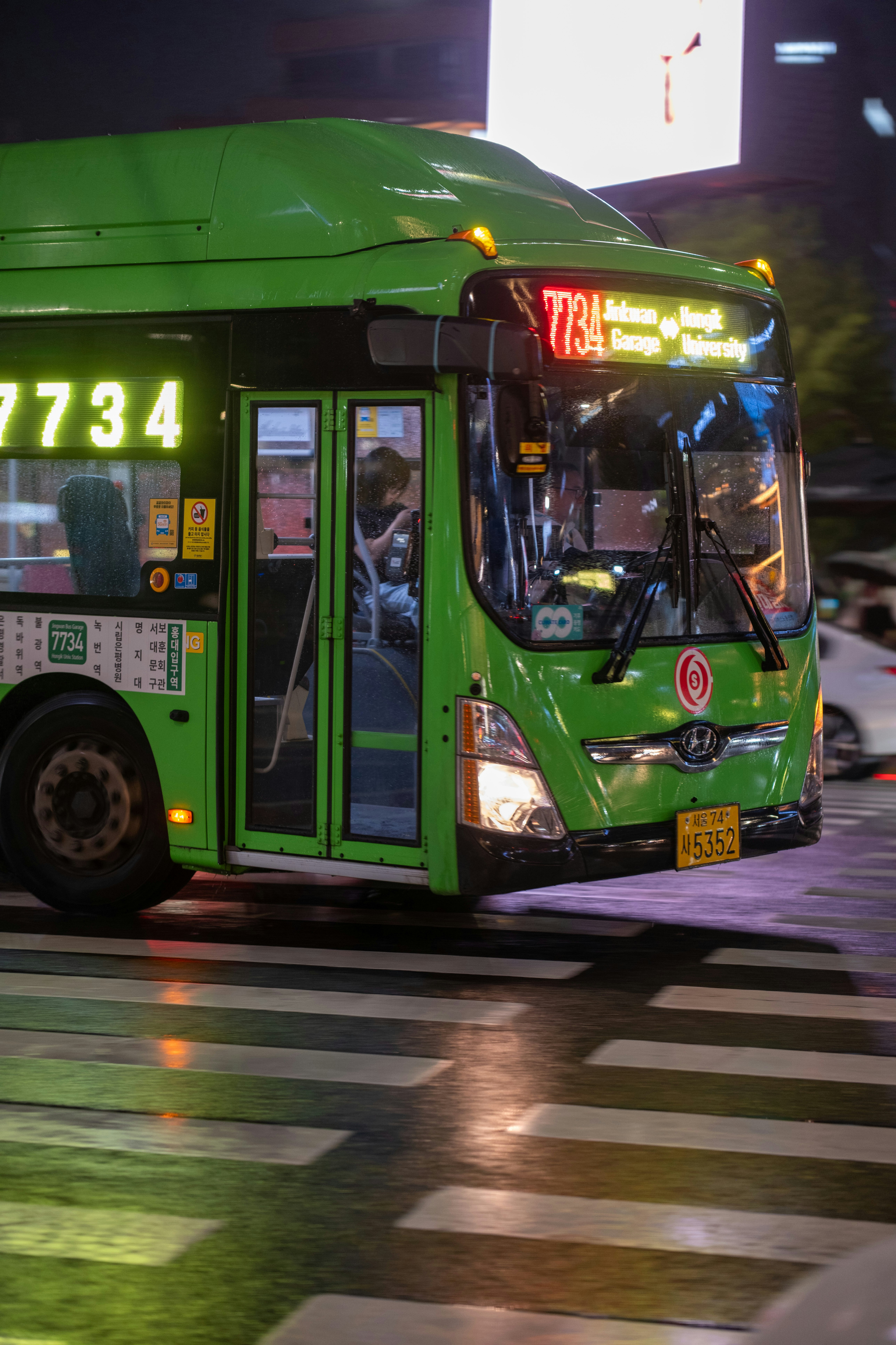 Green bus with illuminated route number drives at night.