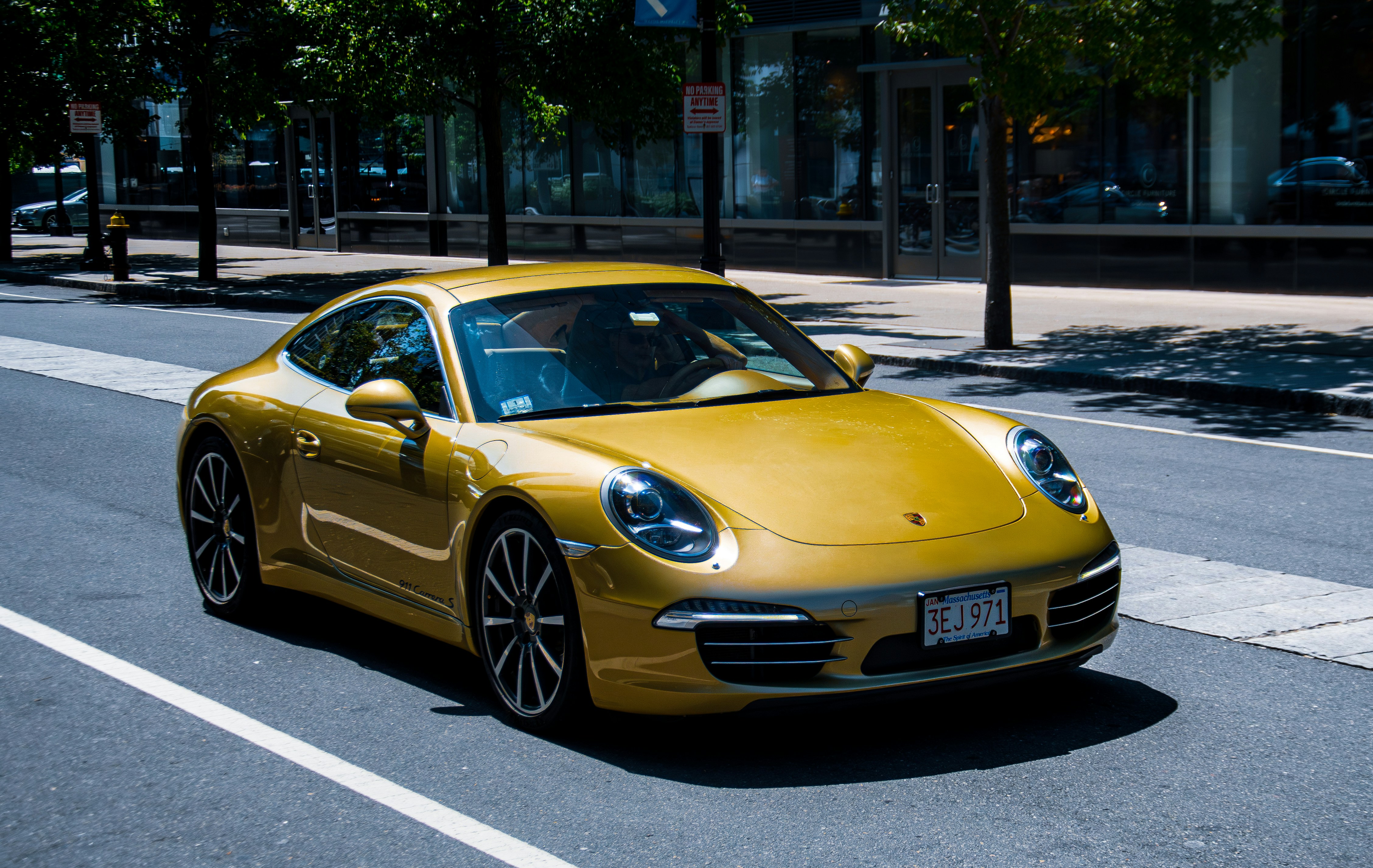 A yellow porsche drives down a city street.