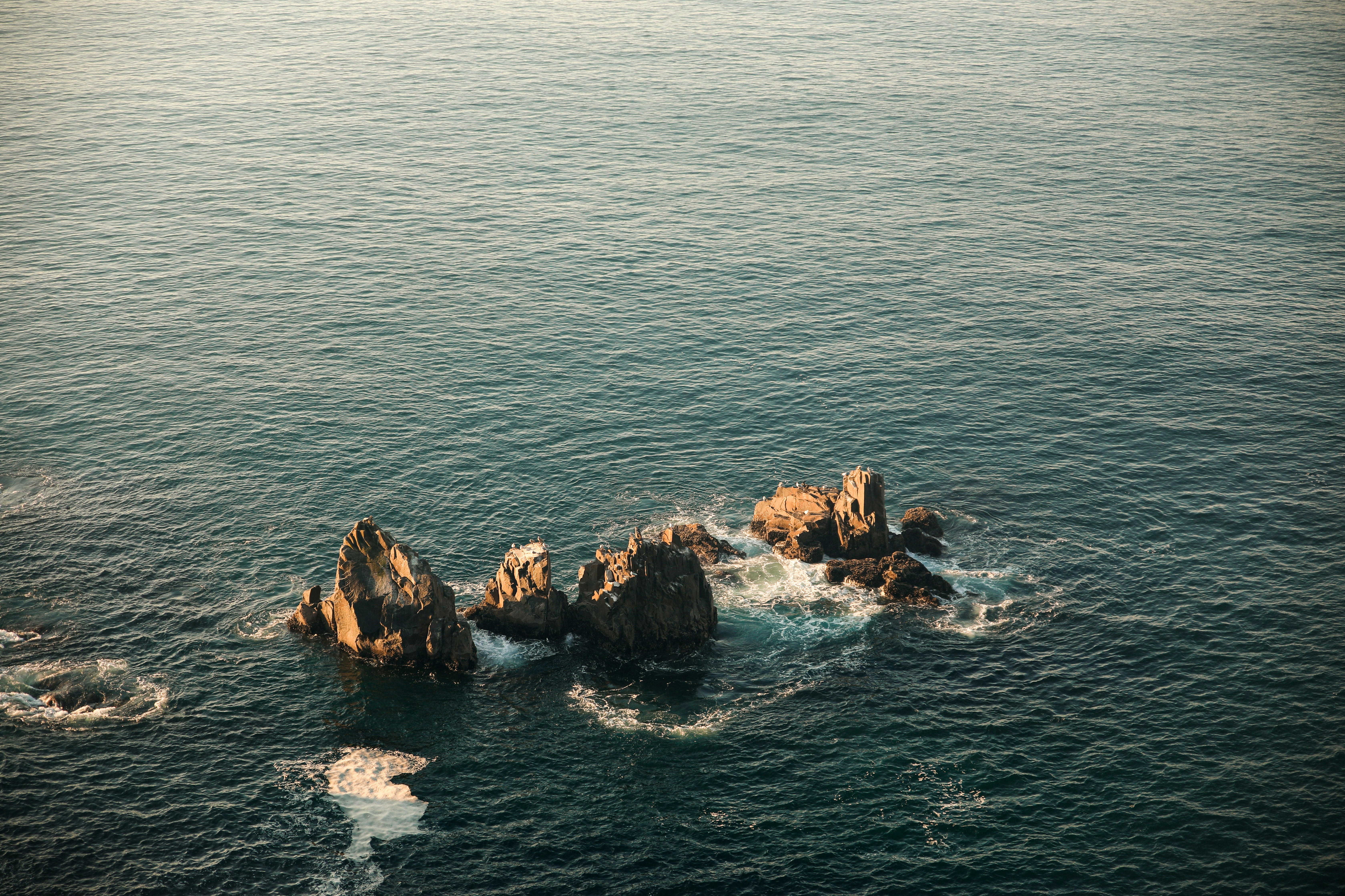Waves crash against rocky outcrops in the ocean.