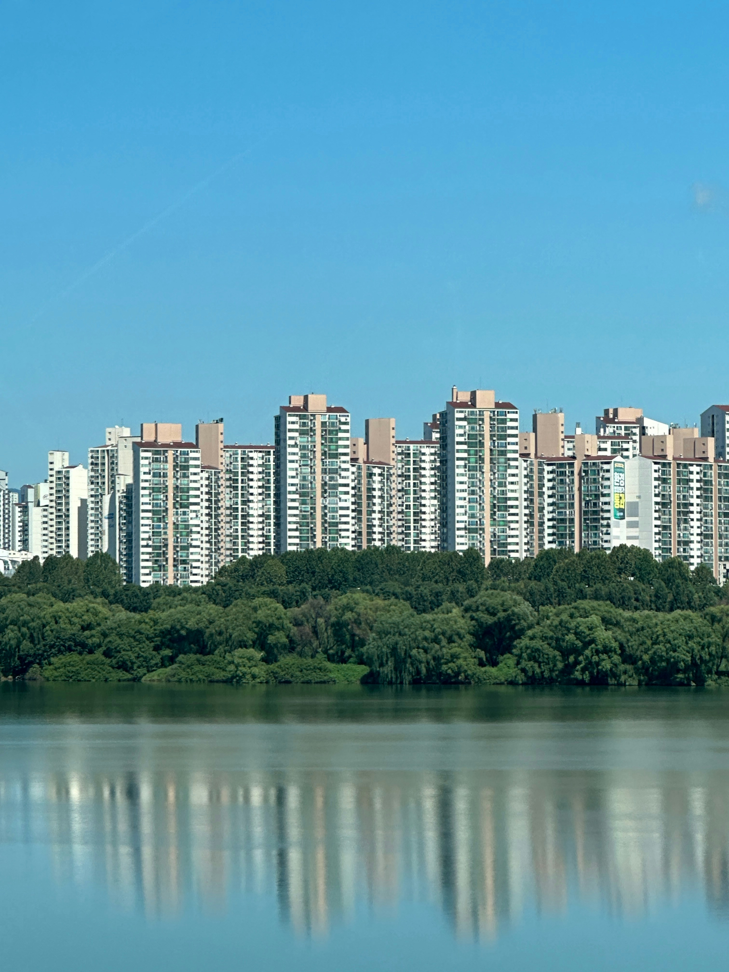 Apartment buildings line a river with green trees.