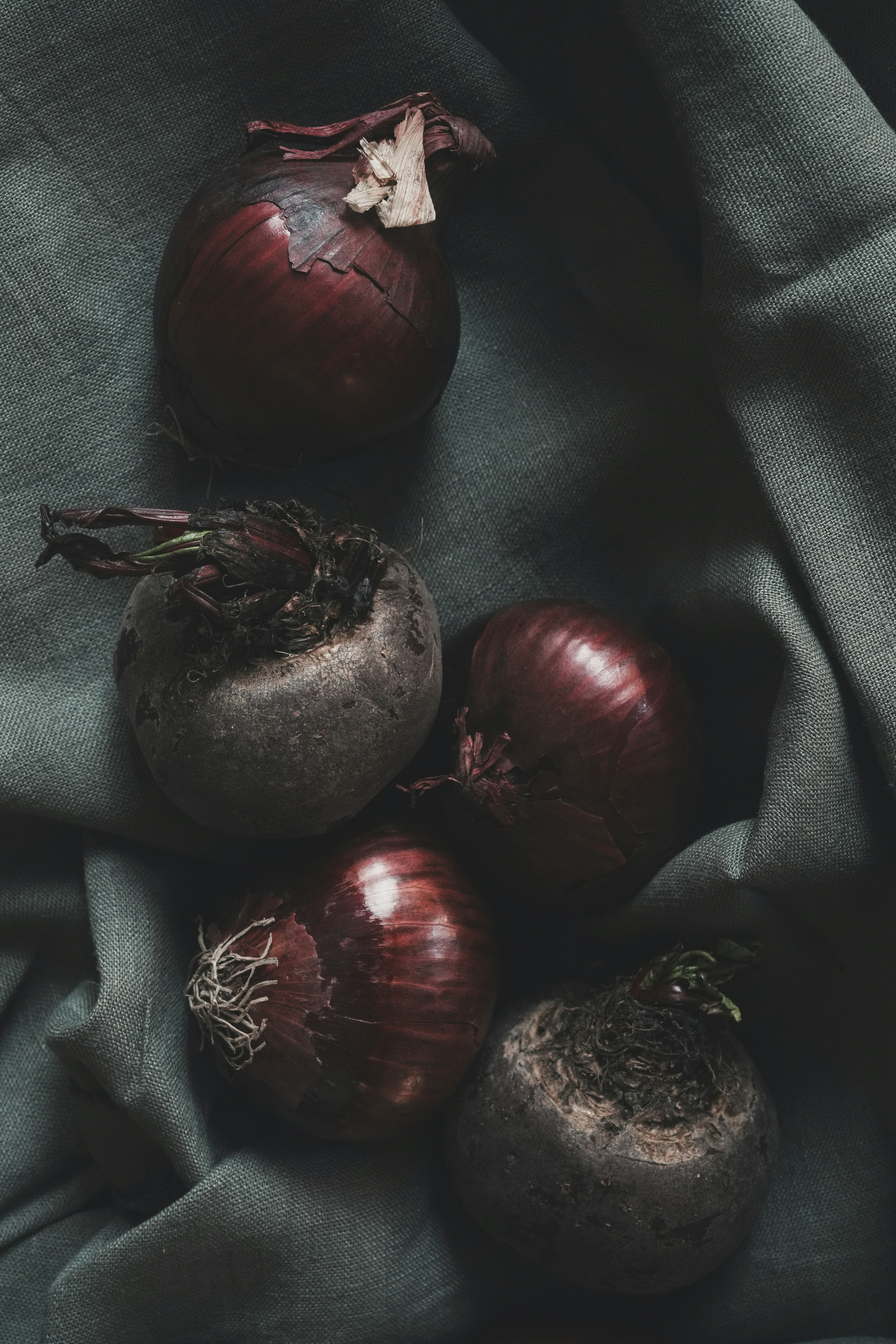 Dark red onions and earthy beets are placed on a soft green fabric | Five red onions and beets arranged on fabric
