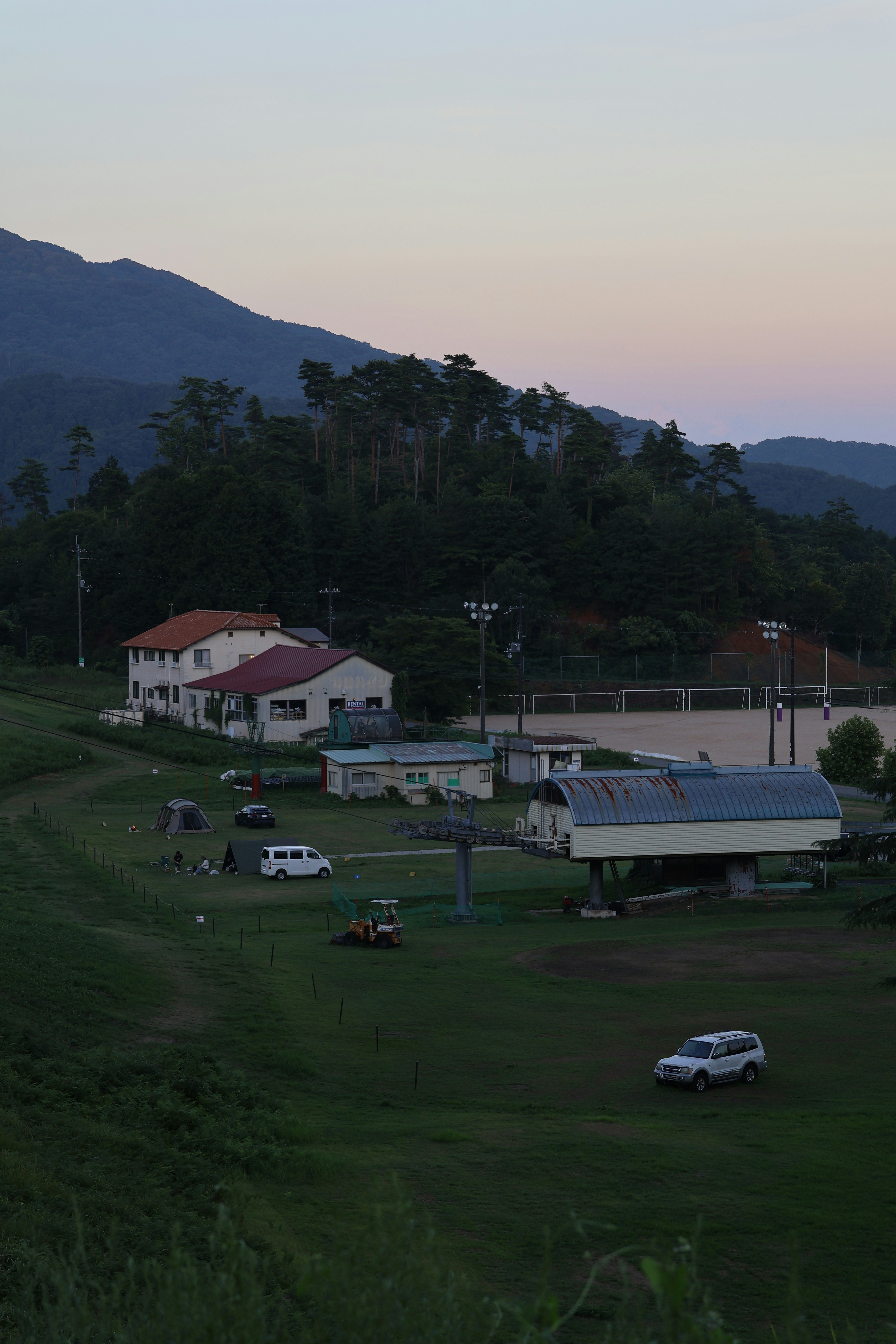 Buildings and ski lift in a grassy landscape at dusk