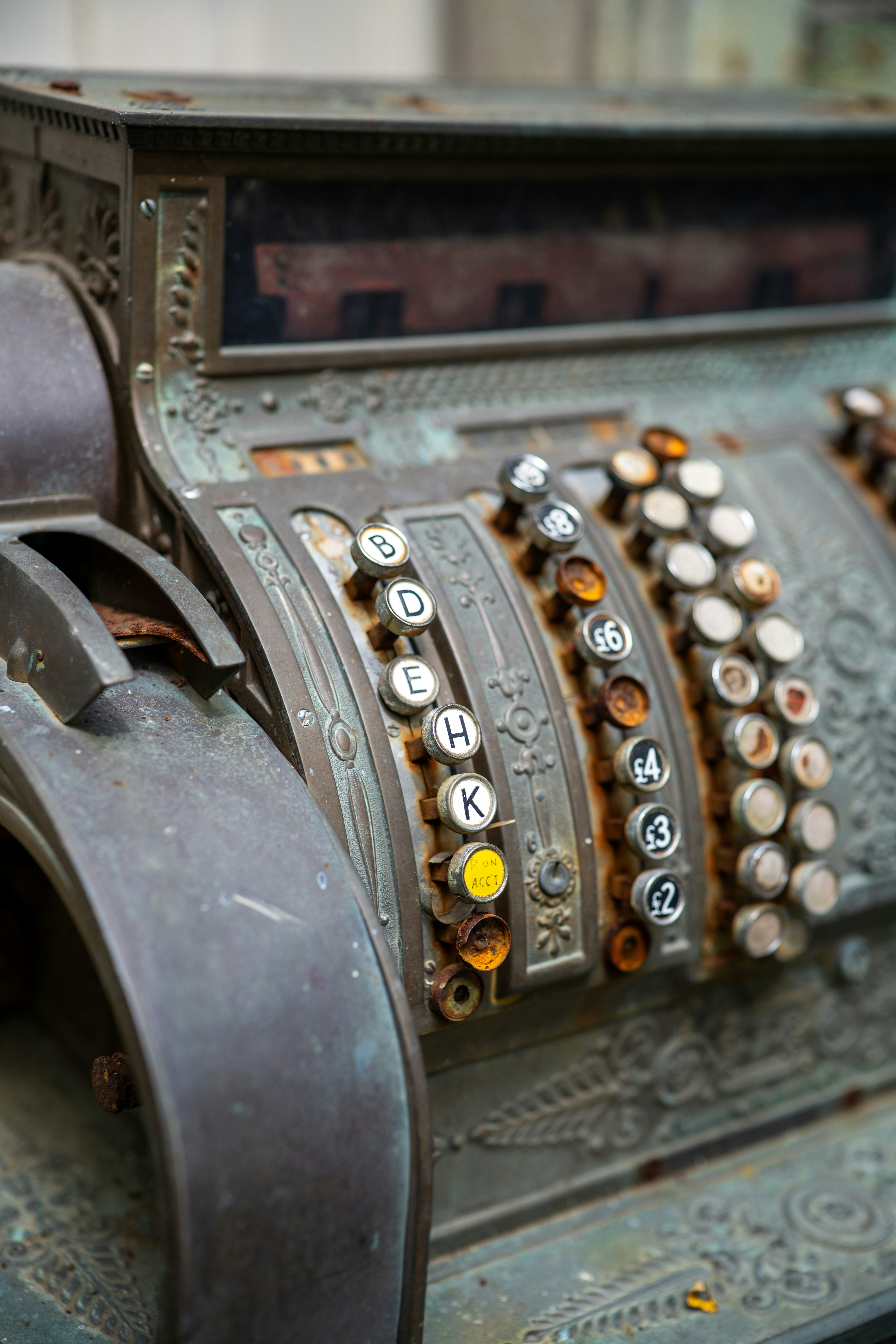 Close-up of a vintage cash register, showcasing its intricate buttons and worn metal detailing. The piece reflects a bygone era of retail history.