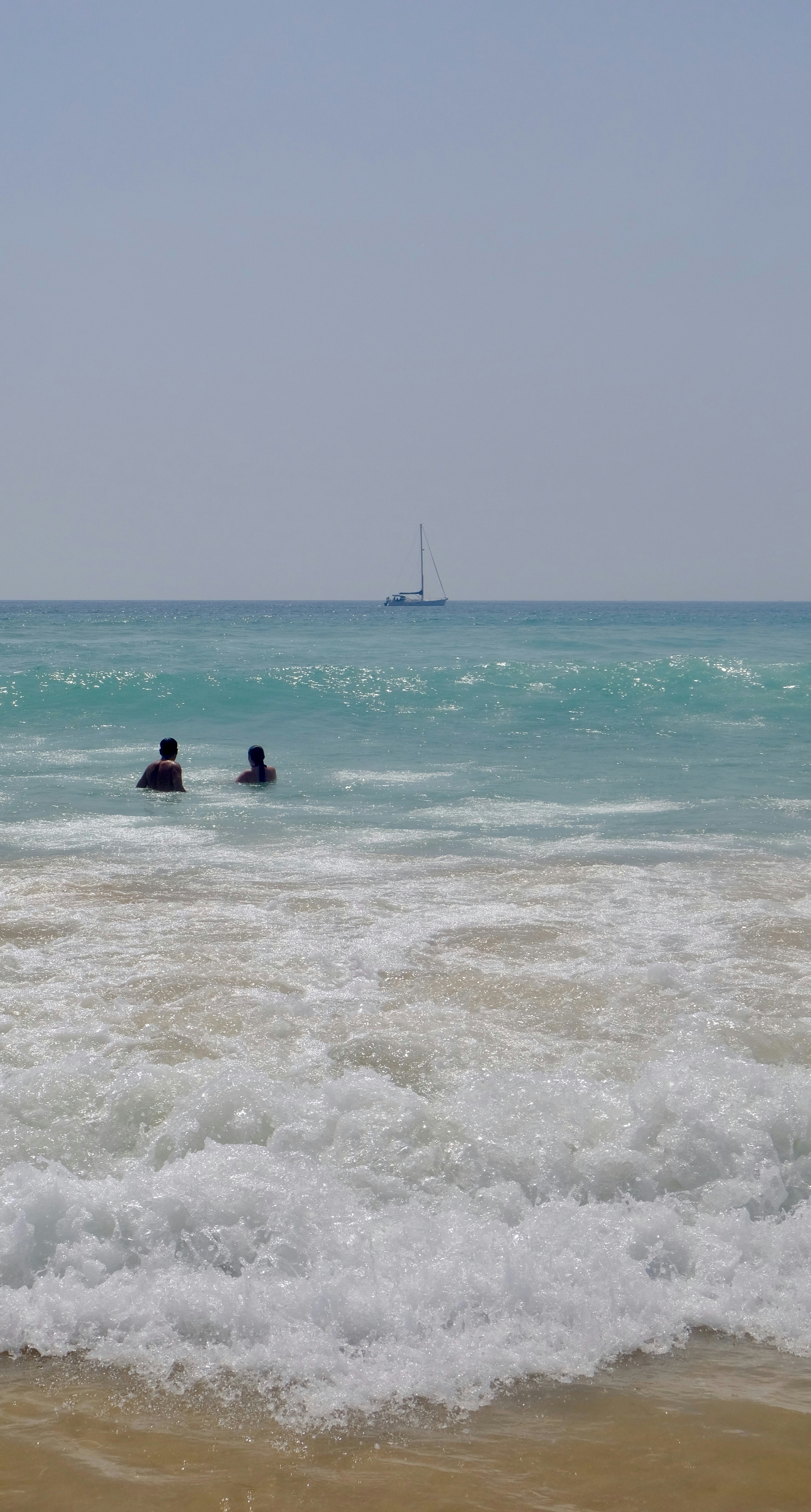 Two Silhouettes in Turquoise: A Quiet Beach Scene with a Distant Sailboat