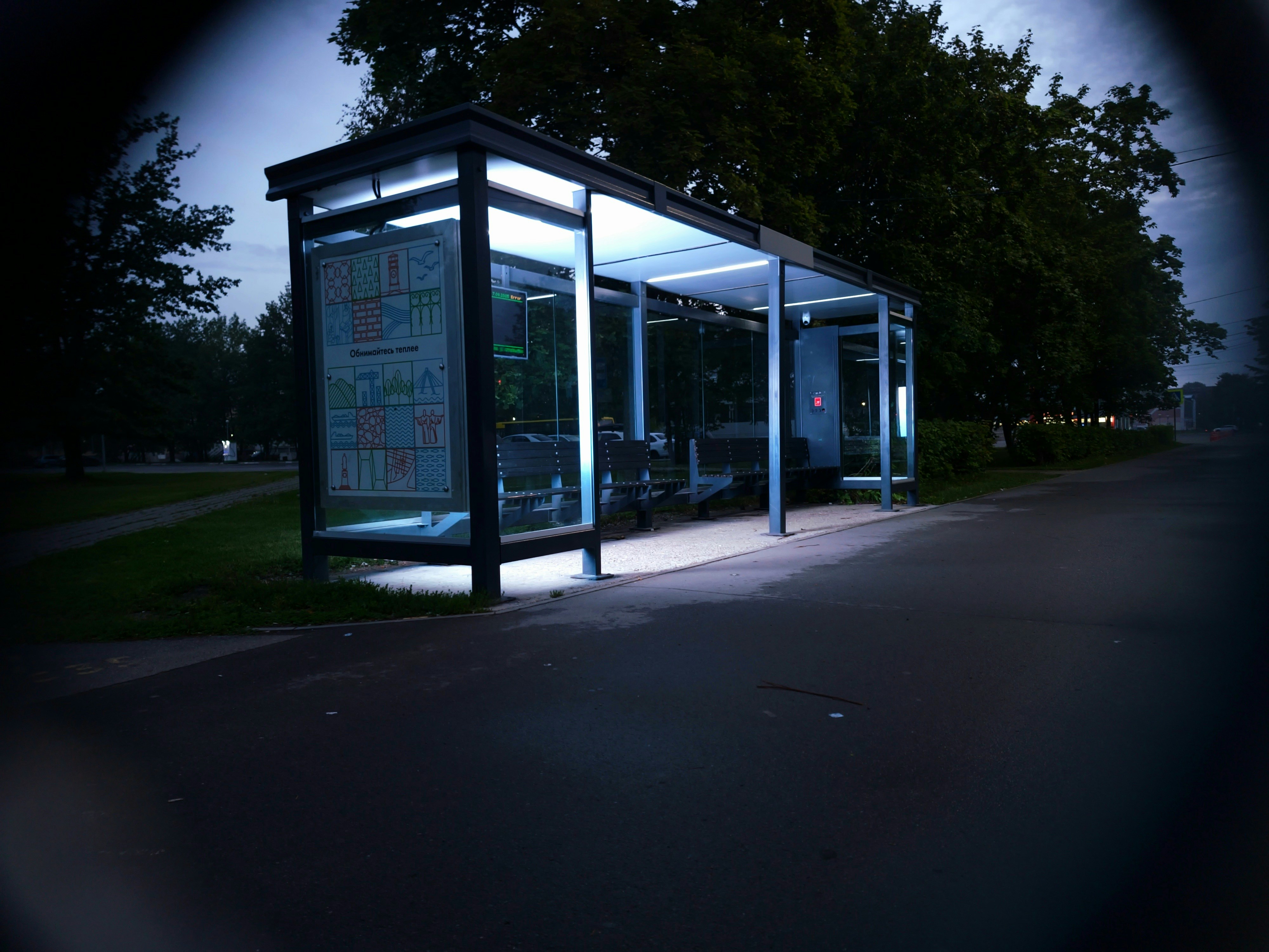 A lone bus stop in the night, | Modern bus stop shelter illuminated at dusk