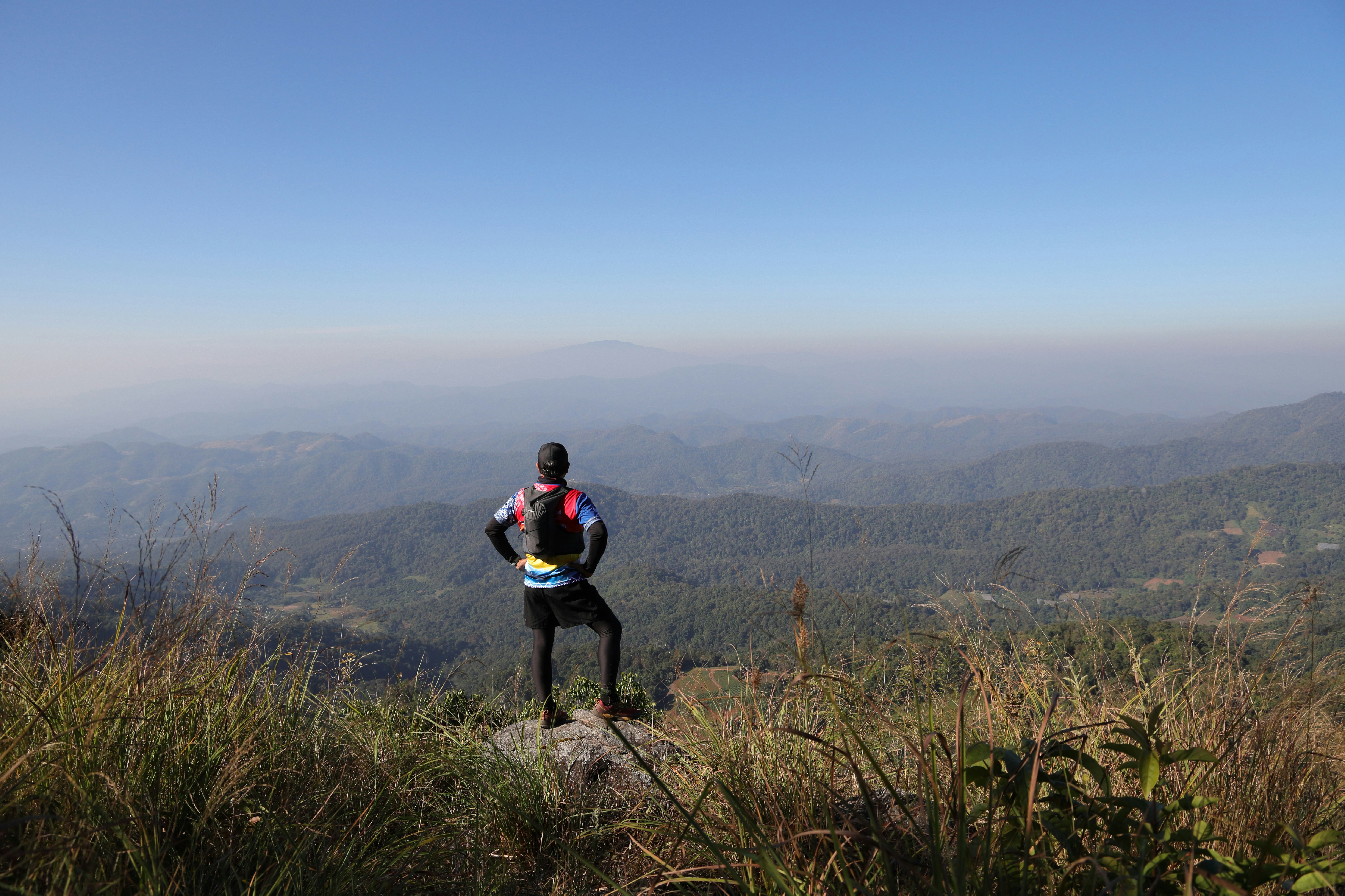Young man hiking outdoors on a trail at Supet-Pui National Park in Chiang Mai, Thailand | Hiker stands on a mountain overlooking a hazy landscape.