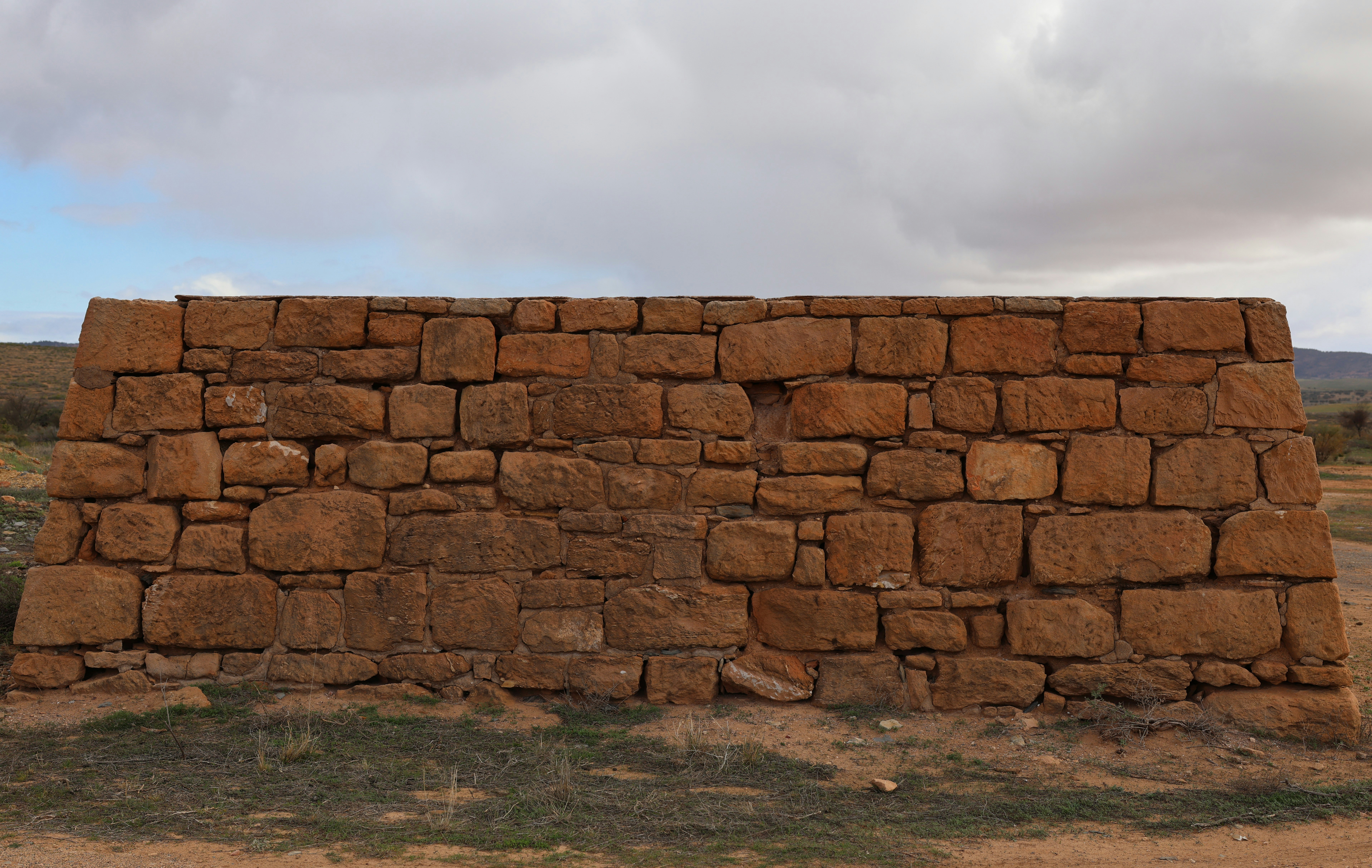 Stone water tank at the abondonded town of Wilson, in north South Australia. | Ancient stone wall under a cloudy sky