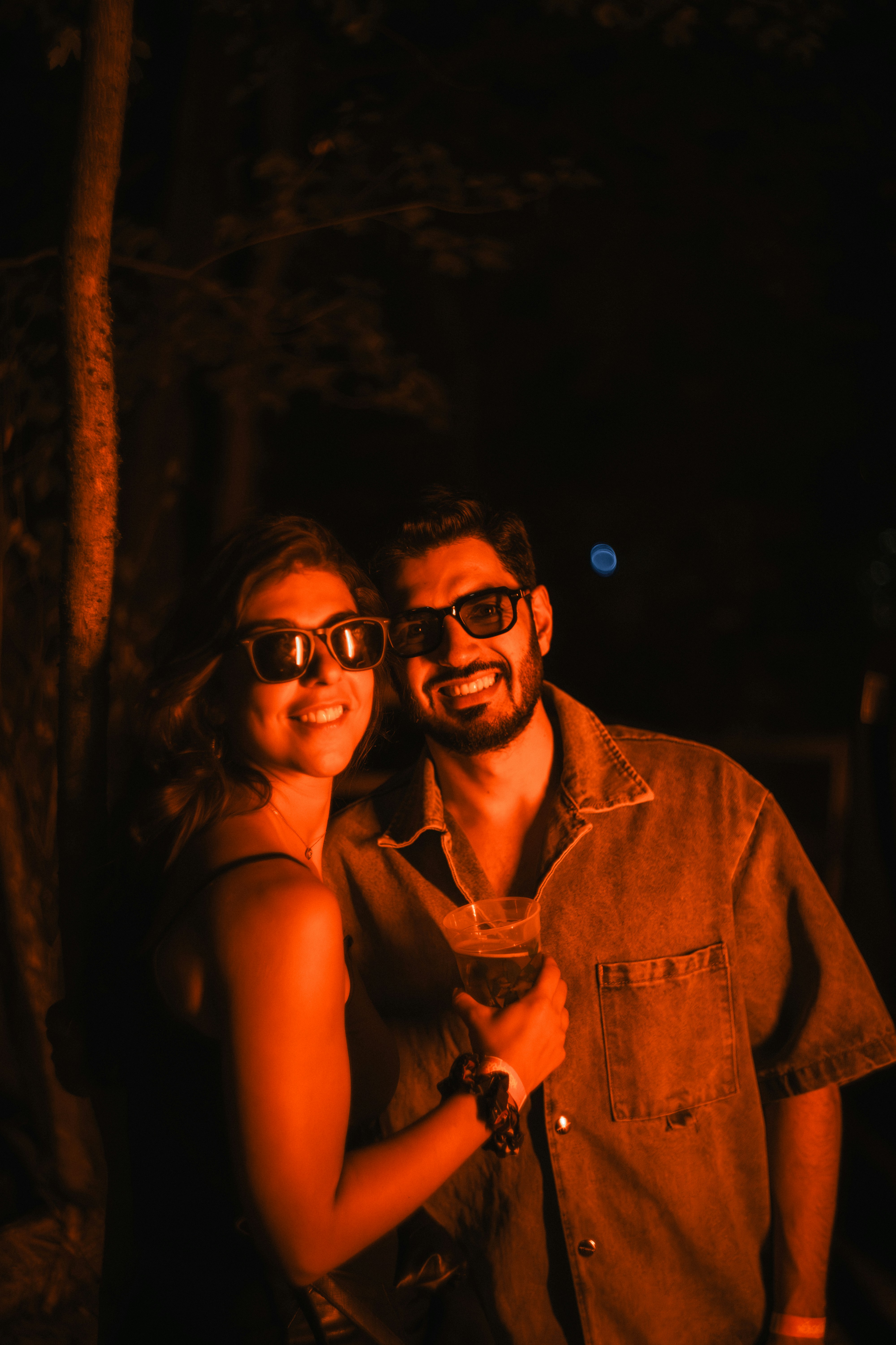 Couple wearing sunglasses at night with warm lighting.