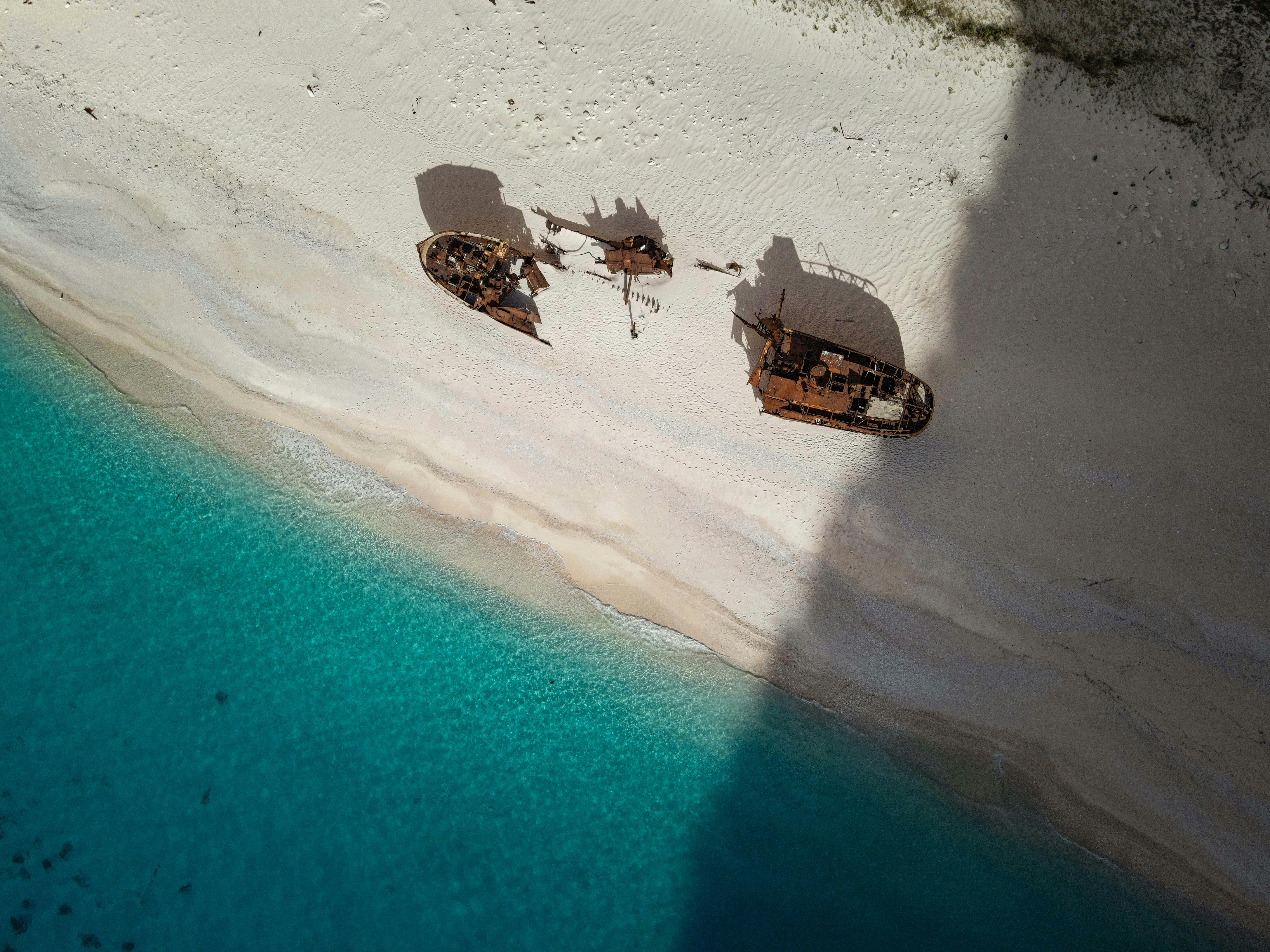 Two weathered shipwrecks rest on a pristine beach, surrounded by turquoise waters and soft sand. The scene captures the contrast between nature and decay.
