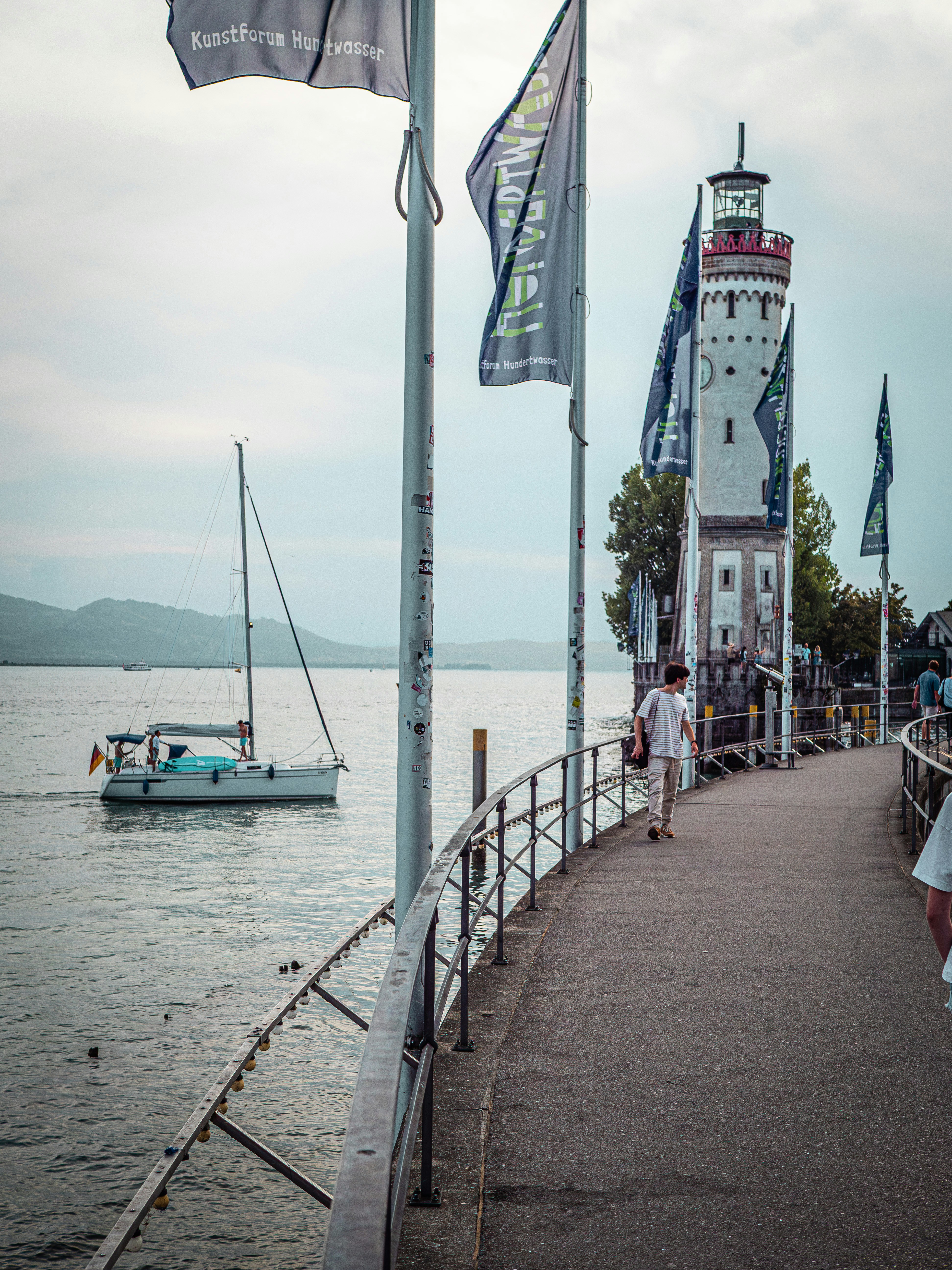 Lighthouse Promenade: Flags, Railings, and a Tranquil Sailboat