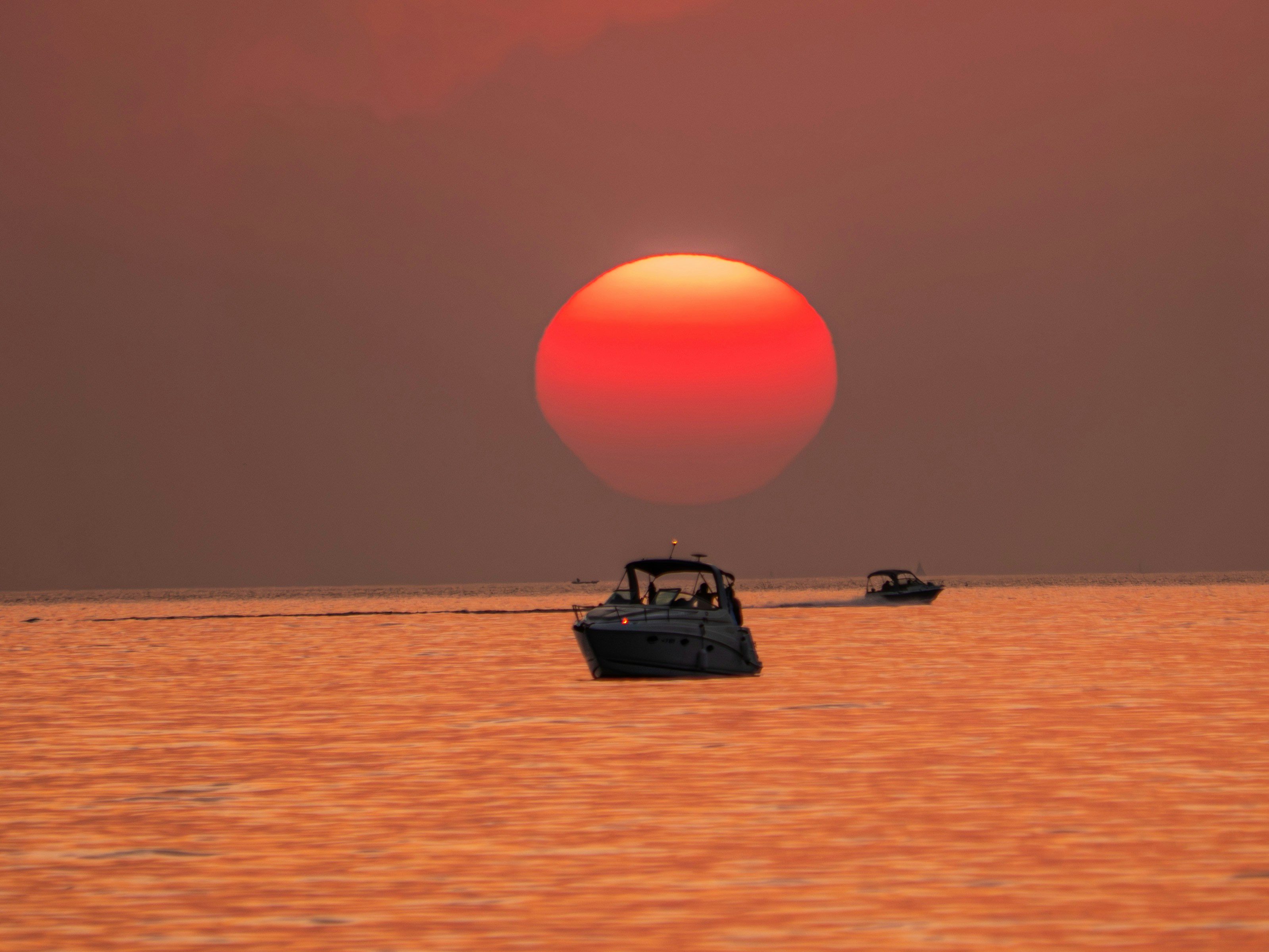 Two boats sail on the ocean during a vibrant sunset