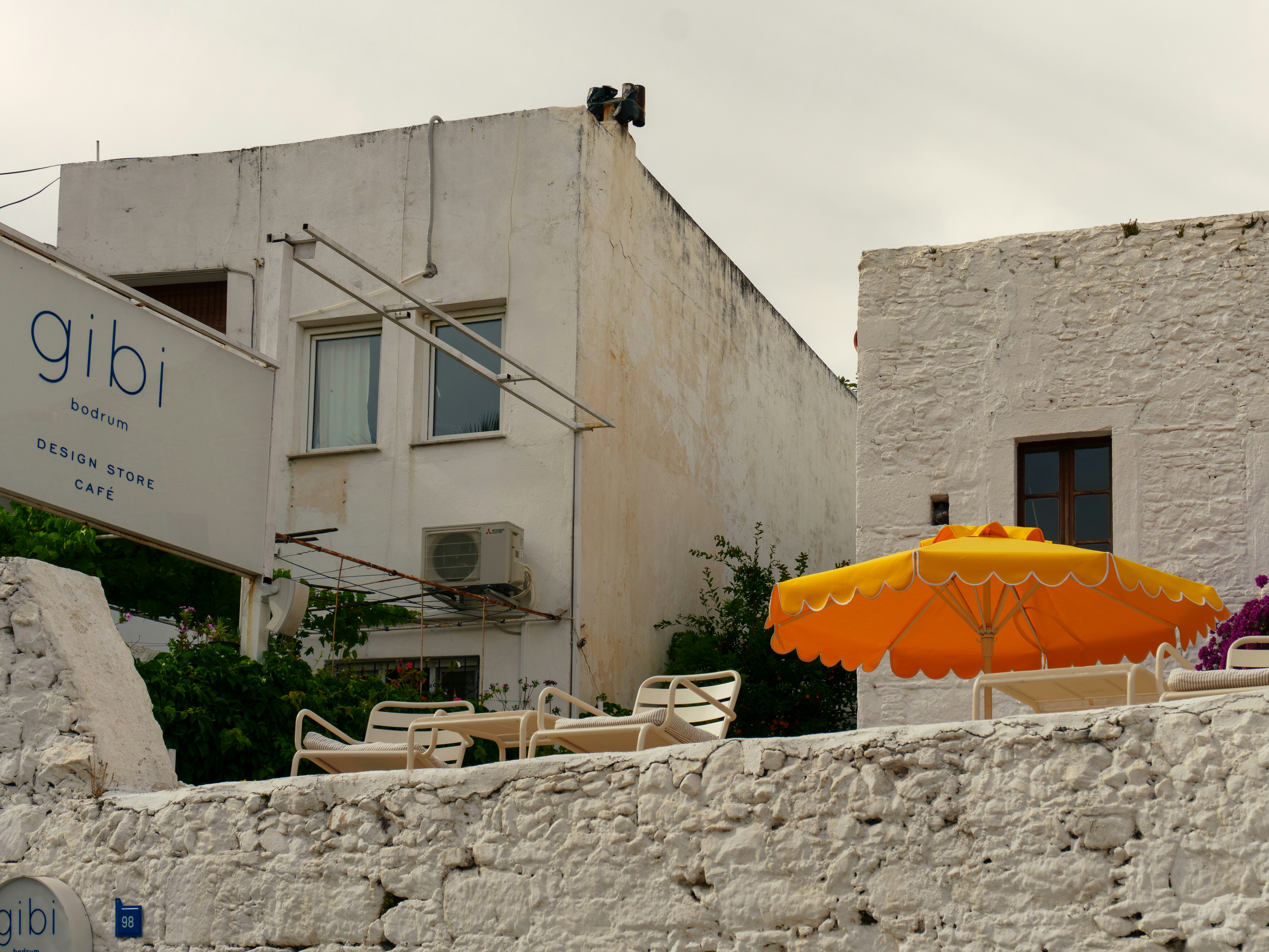 Vibrant yellow umbrella shading outdoor seating at a café, framed by whitewashed buildings and lush greenery.