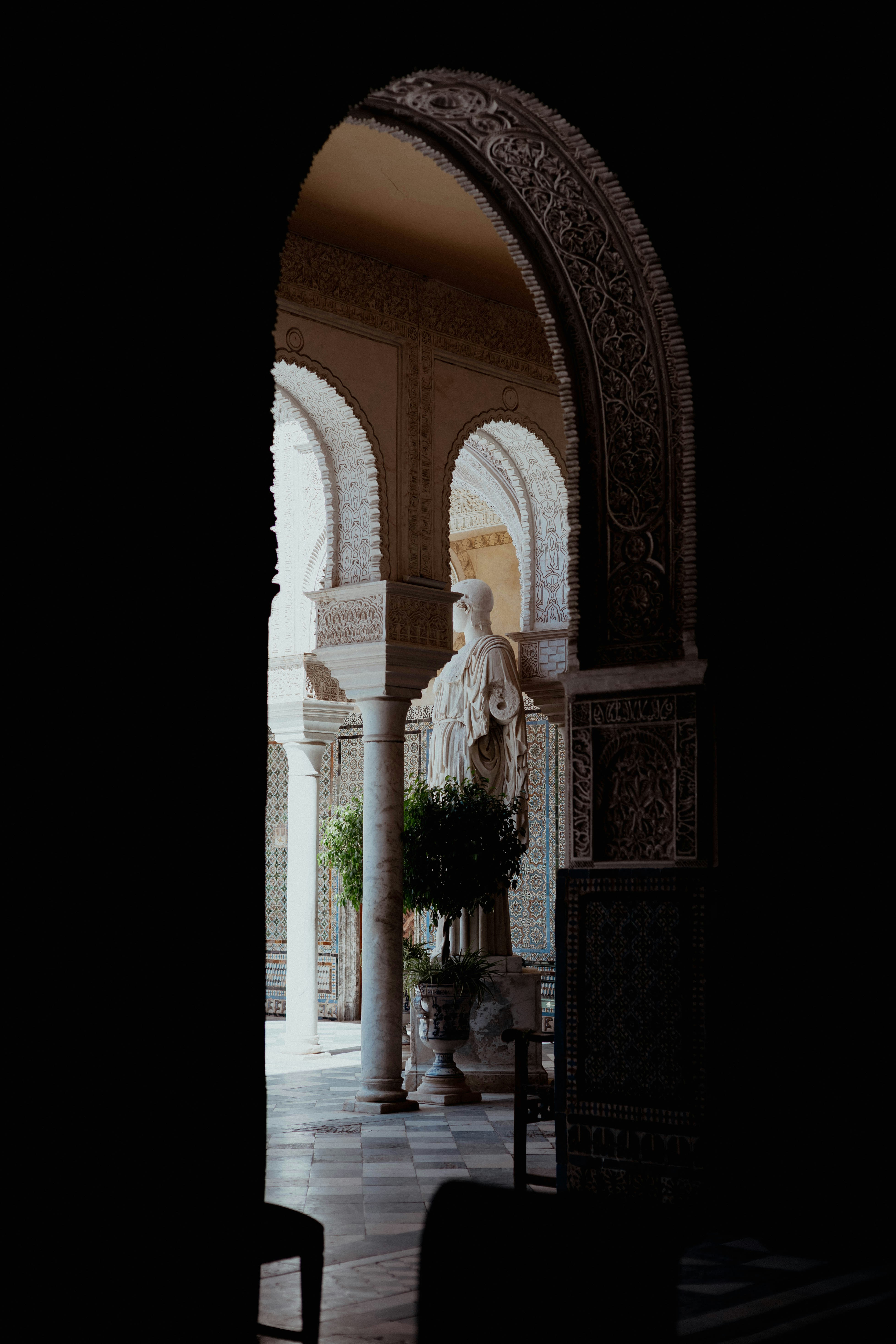 Ornate archway reveals courtyard with statue and plants