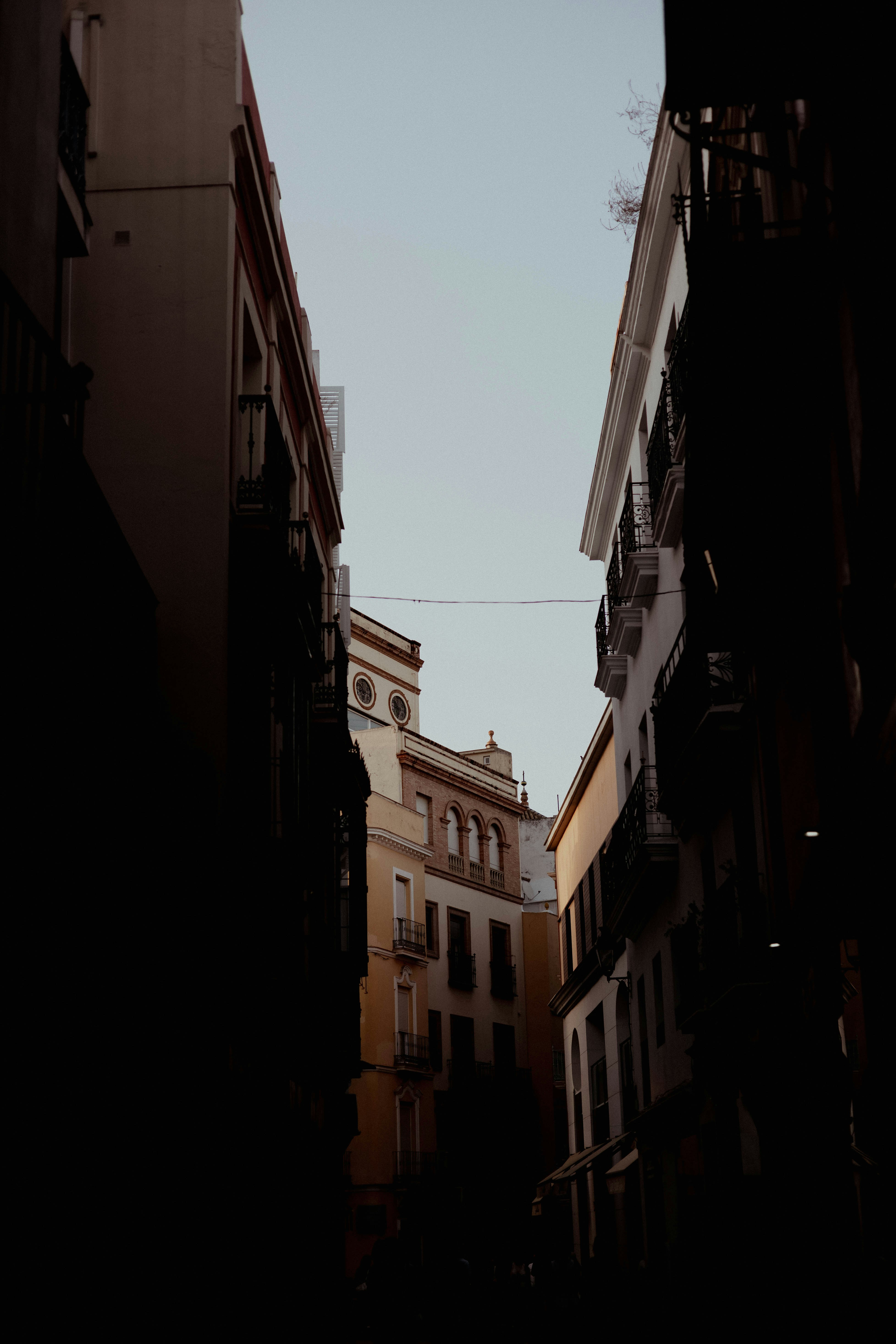 Narrow alleyway framed by tall buildings, revealing a glimpse of a distant architectural feature against a pale sky.